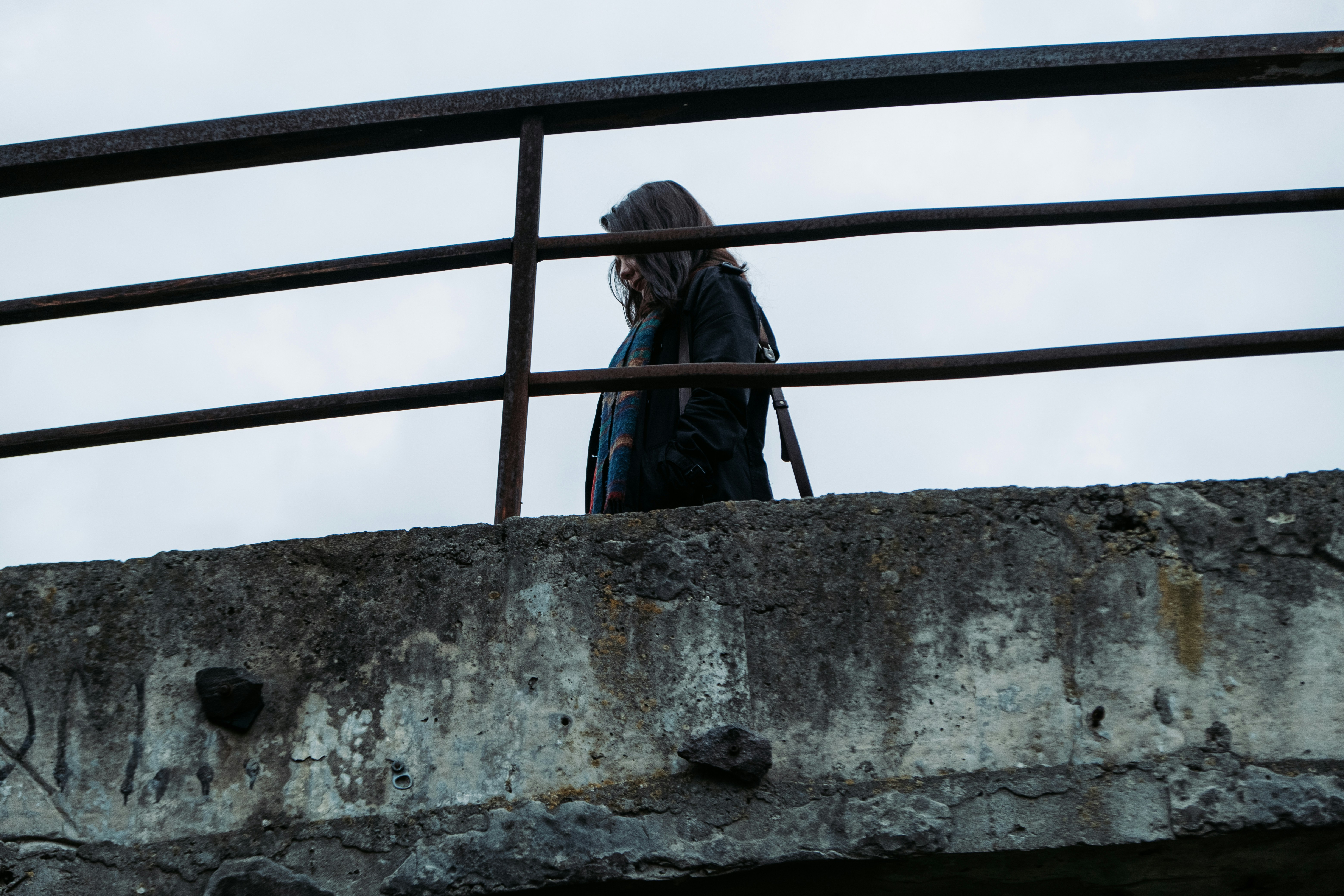woman in blue jacket standing on gray concrete wall during daytime