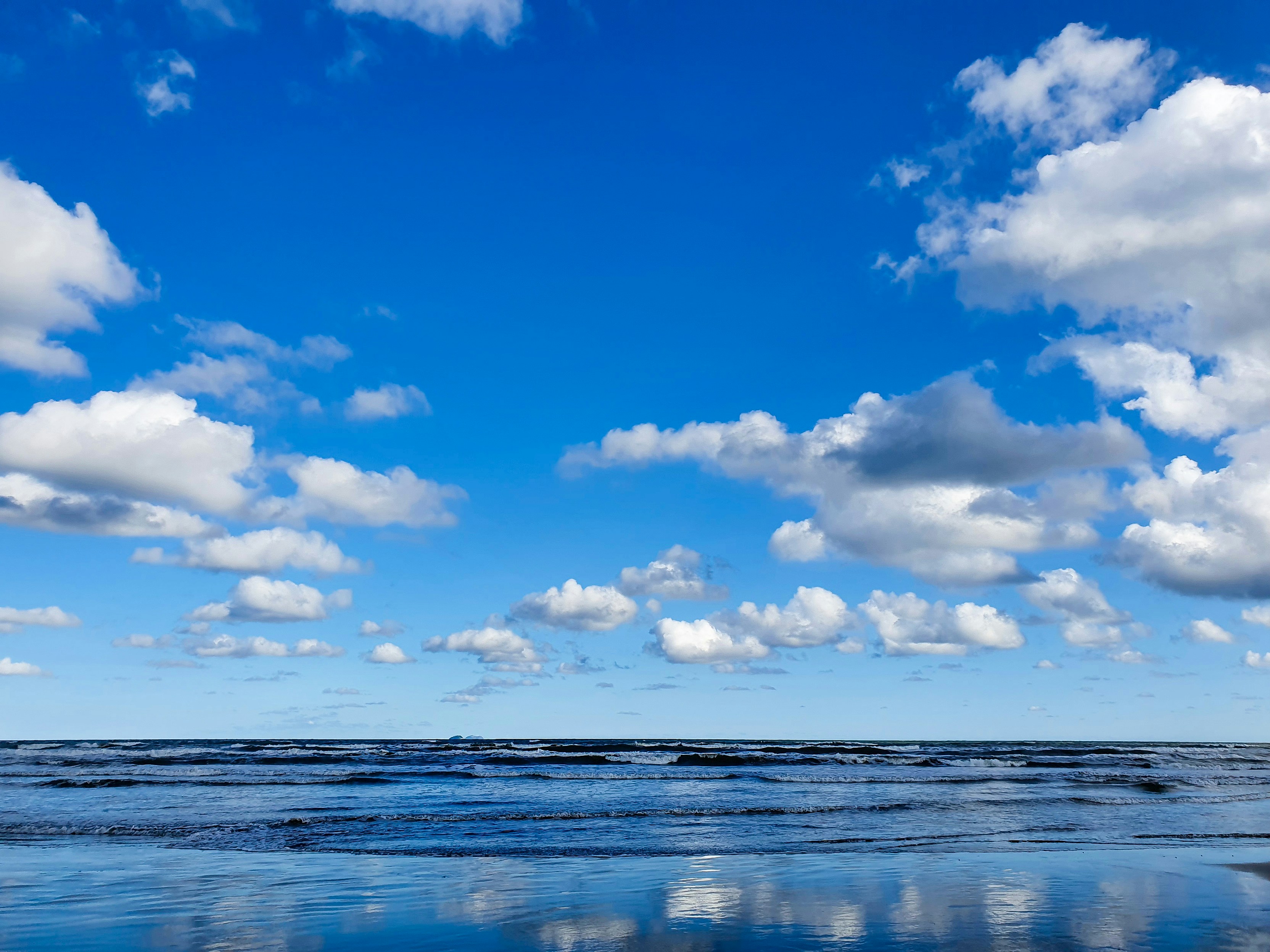 Vast ocean surface reflecting a brilliant blue sky dotted with fluffy clouds, creating a serene atmosphere.