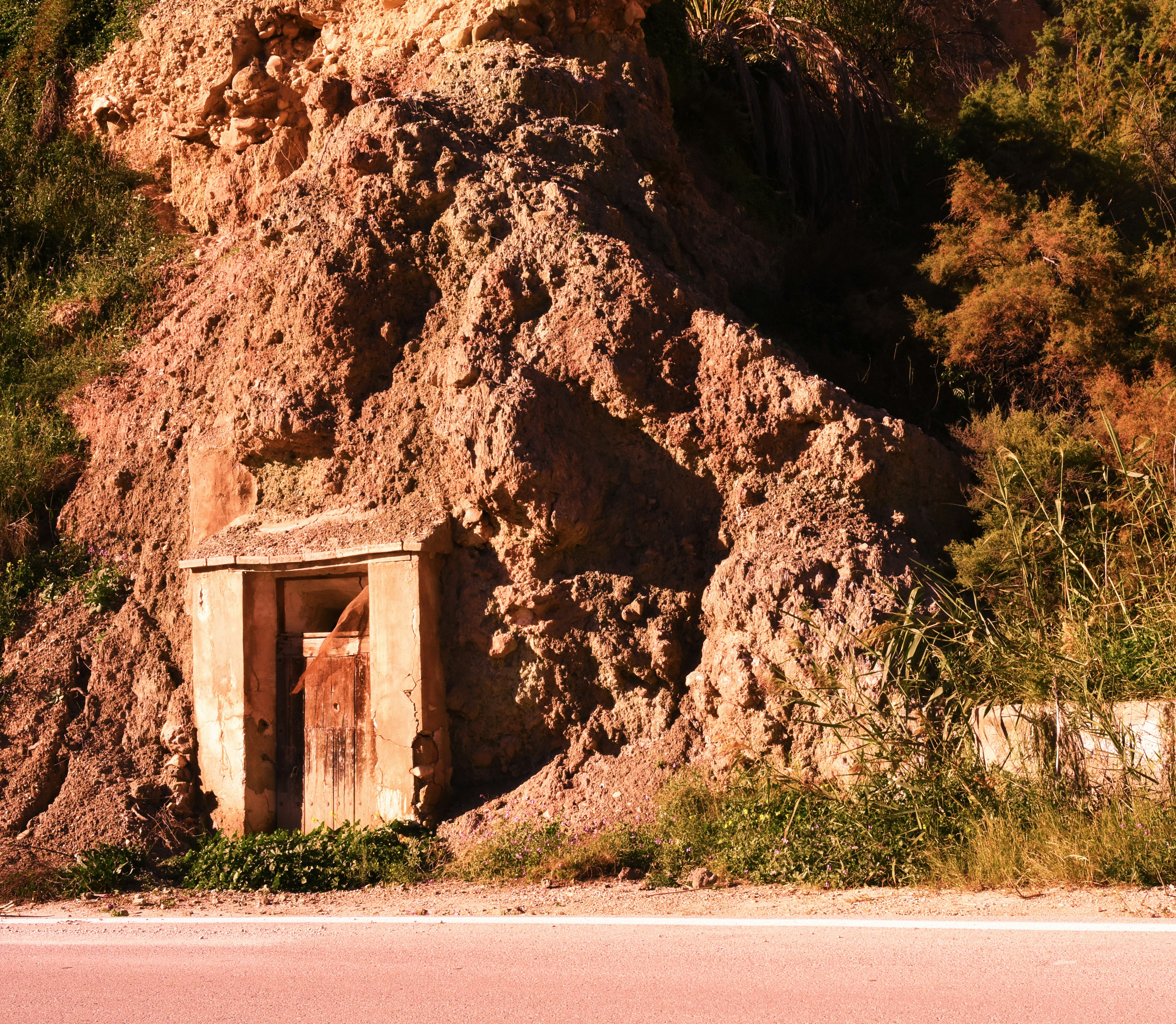 Rustic doorway embedded in a rocky hillside with sparse vegetation under bright sunlight.