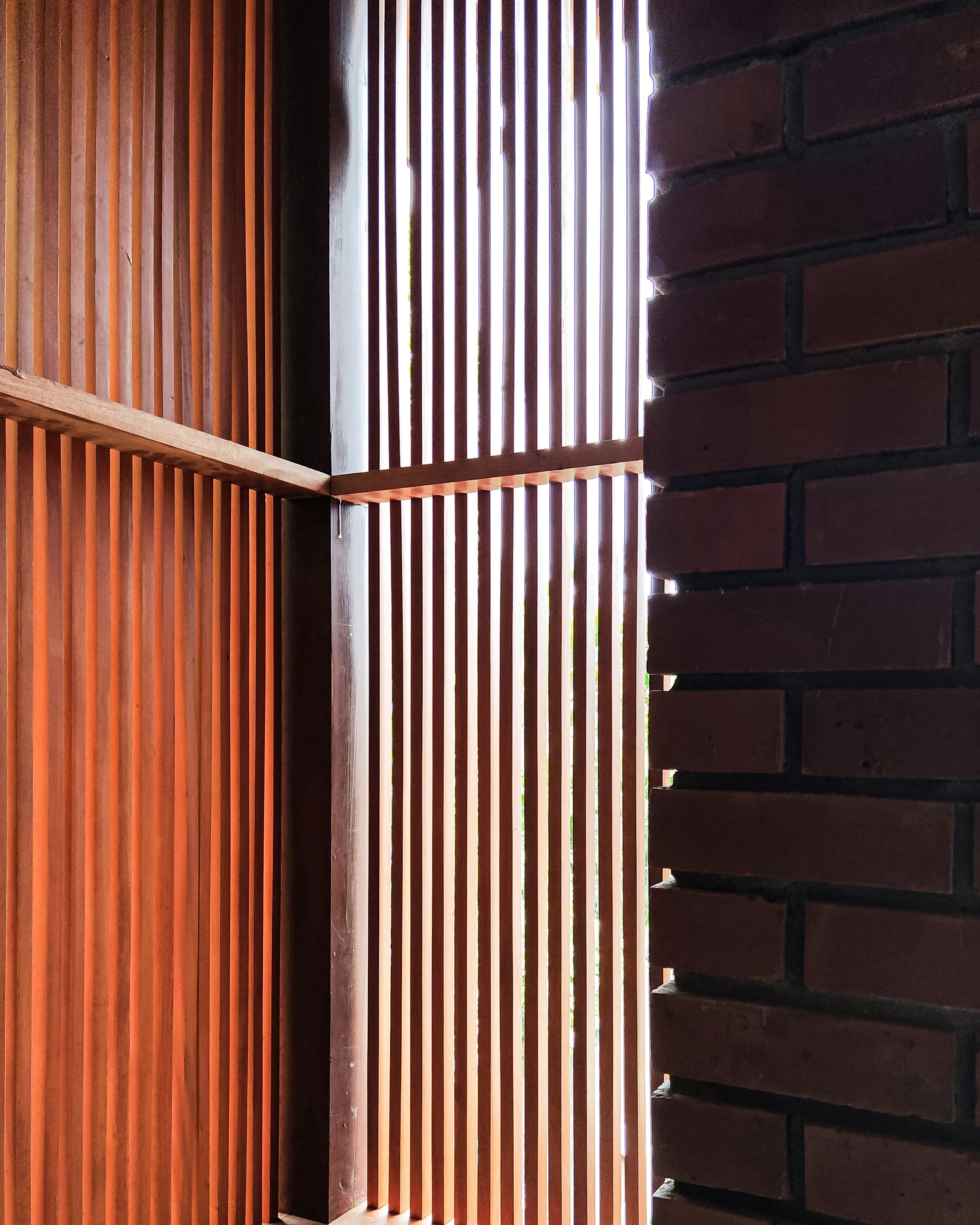 Sunlight filters through vertical wooden slats beside a brick wall, creating a pattern of light and shadow.