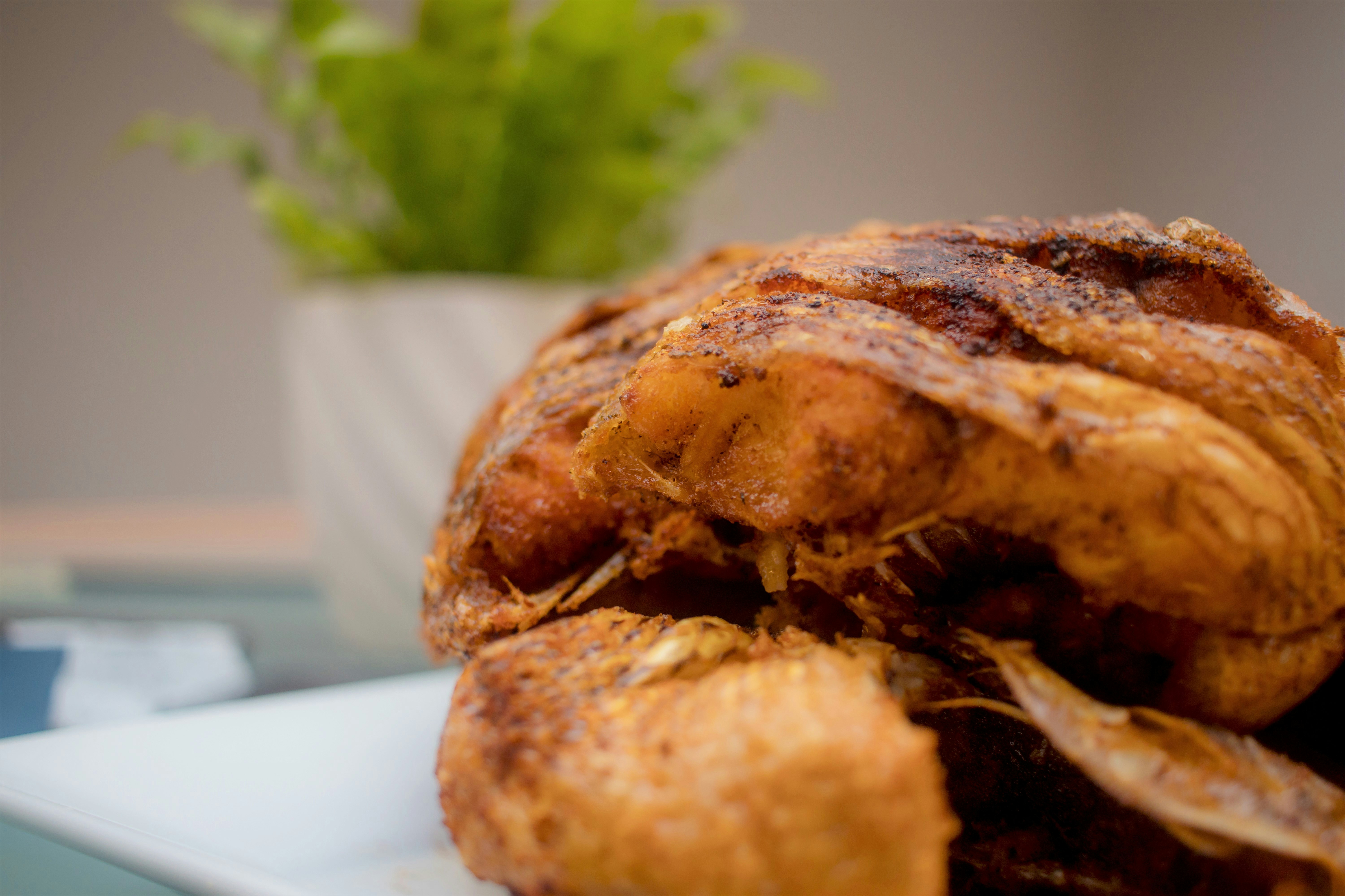 Fried tilapia on a white plate with blurred greenery in the background.