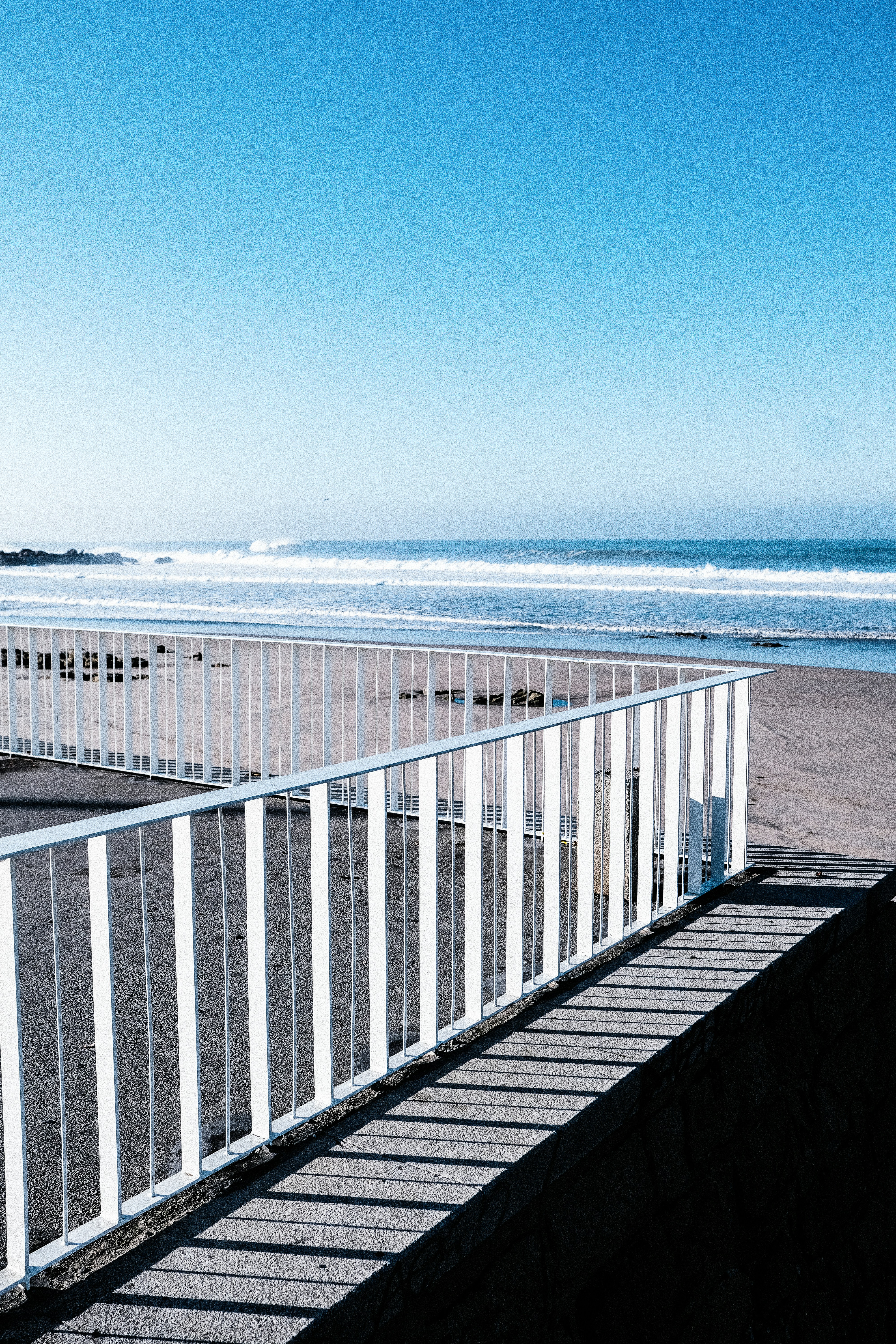 Leading Lines to the Sea: White Railings Frame a Quiet Beach Horizon