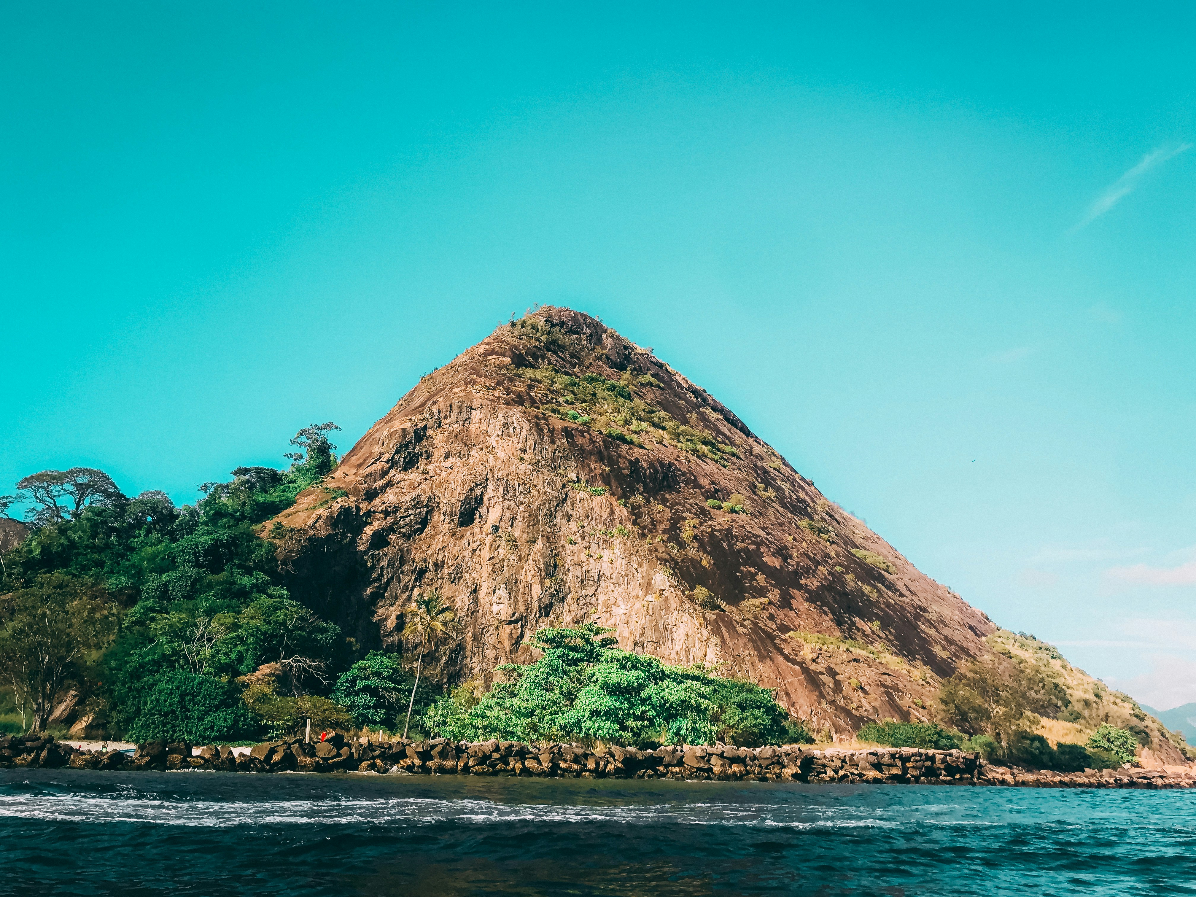 Steep brown hill rises beside vibrant turquoise waters under a clear sky.