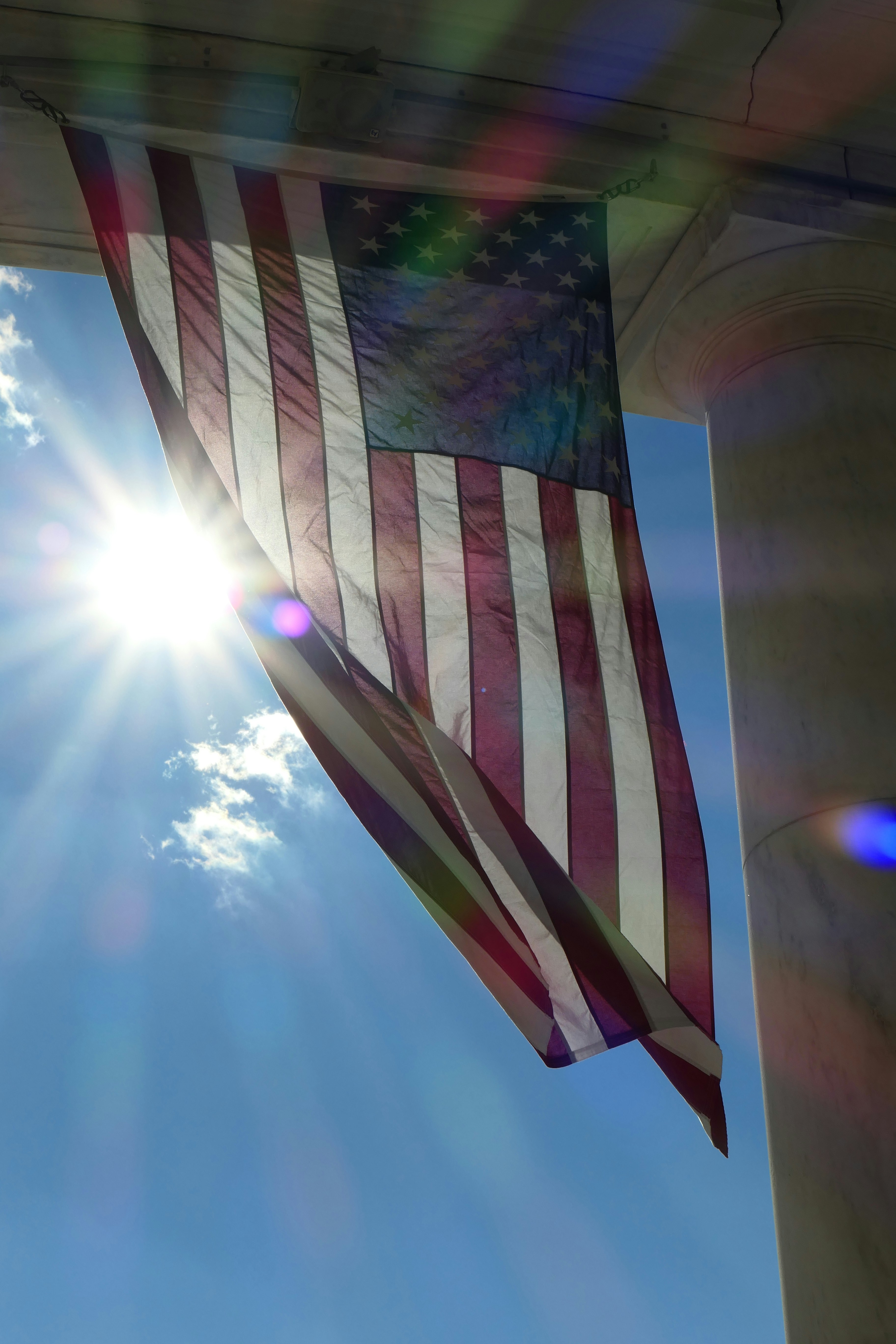 American flag billowing in the breeze against a bright sky, with sunlight creating a radiant starburst effect. 
