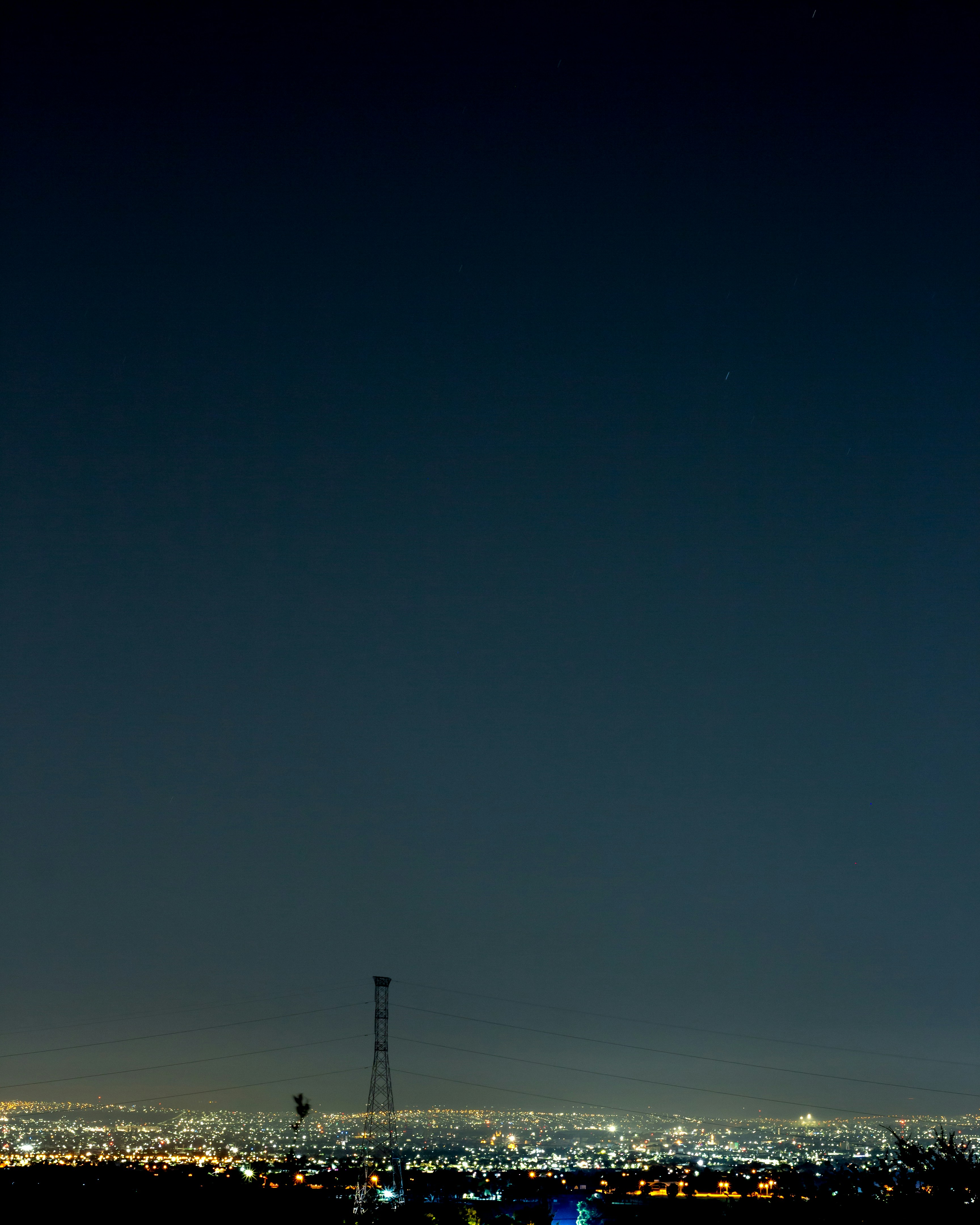 Night city skyline glows along the horizon, with a transmission tower and power lines framing the foreground.
