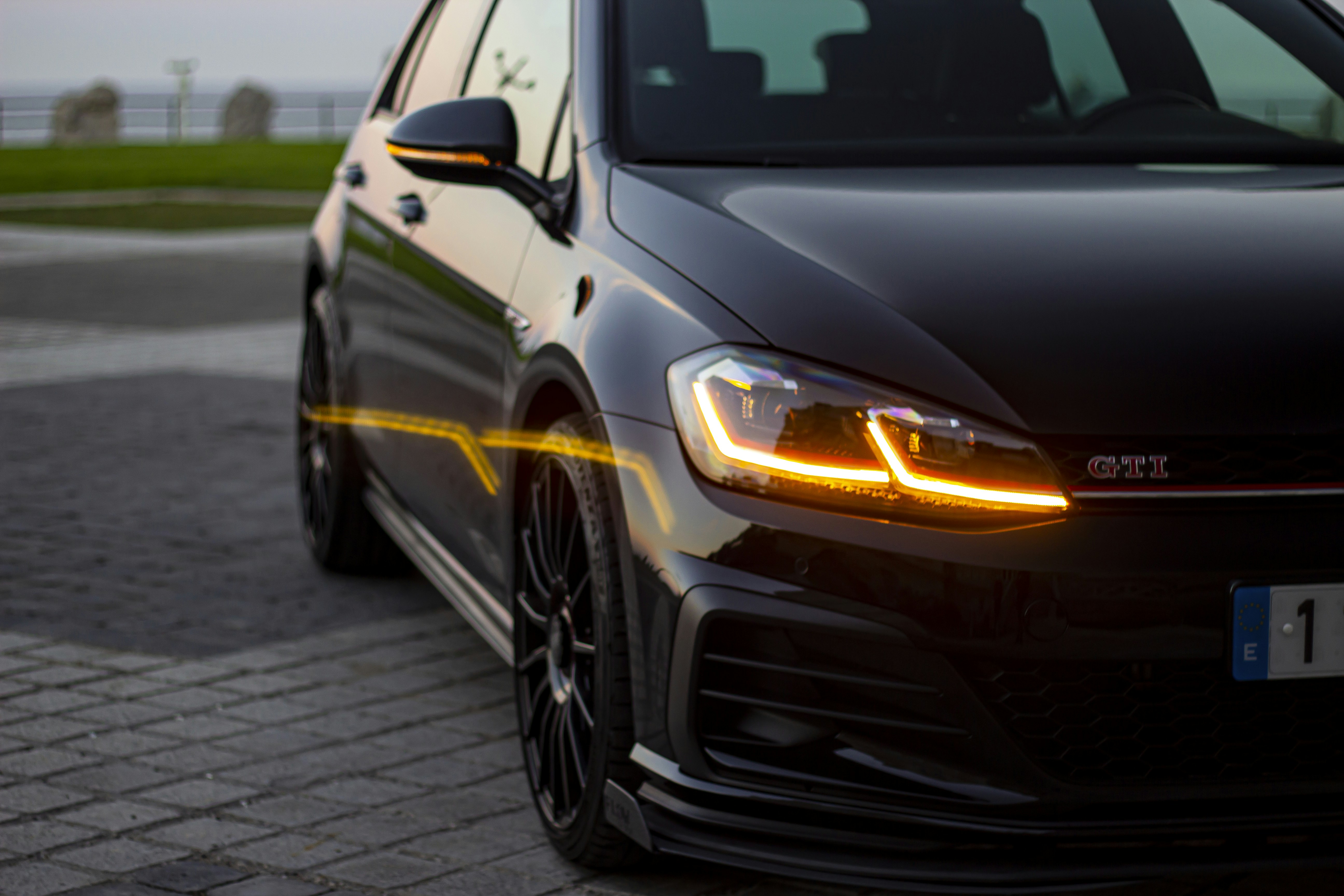 Sleek black Volkswagen GTI with illuminated headlights parked on a cobblestone surface, showcasing its striking design and sporty character.