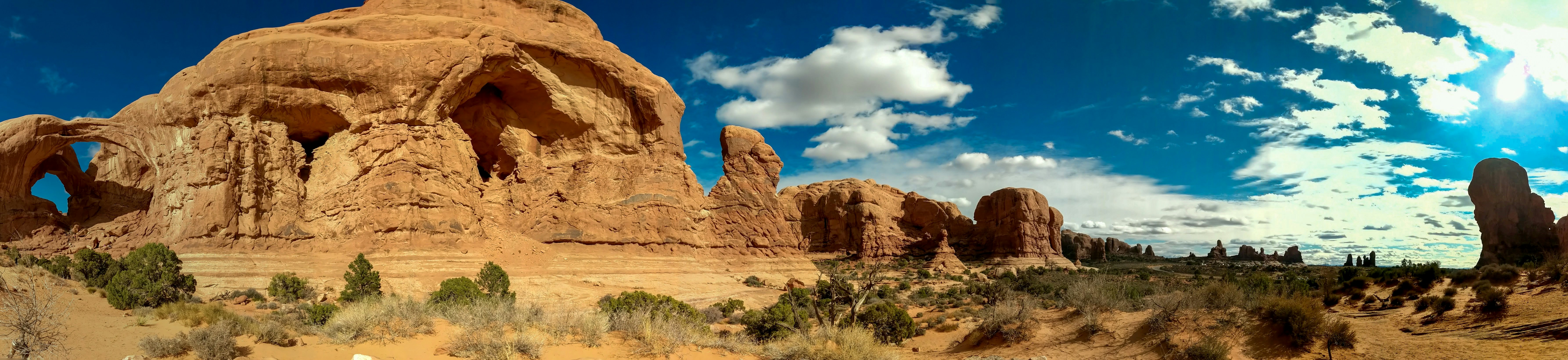 Expansive rock formations with natural arches beneath a bright blue sky dotted with clouds.