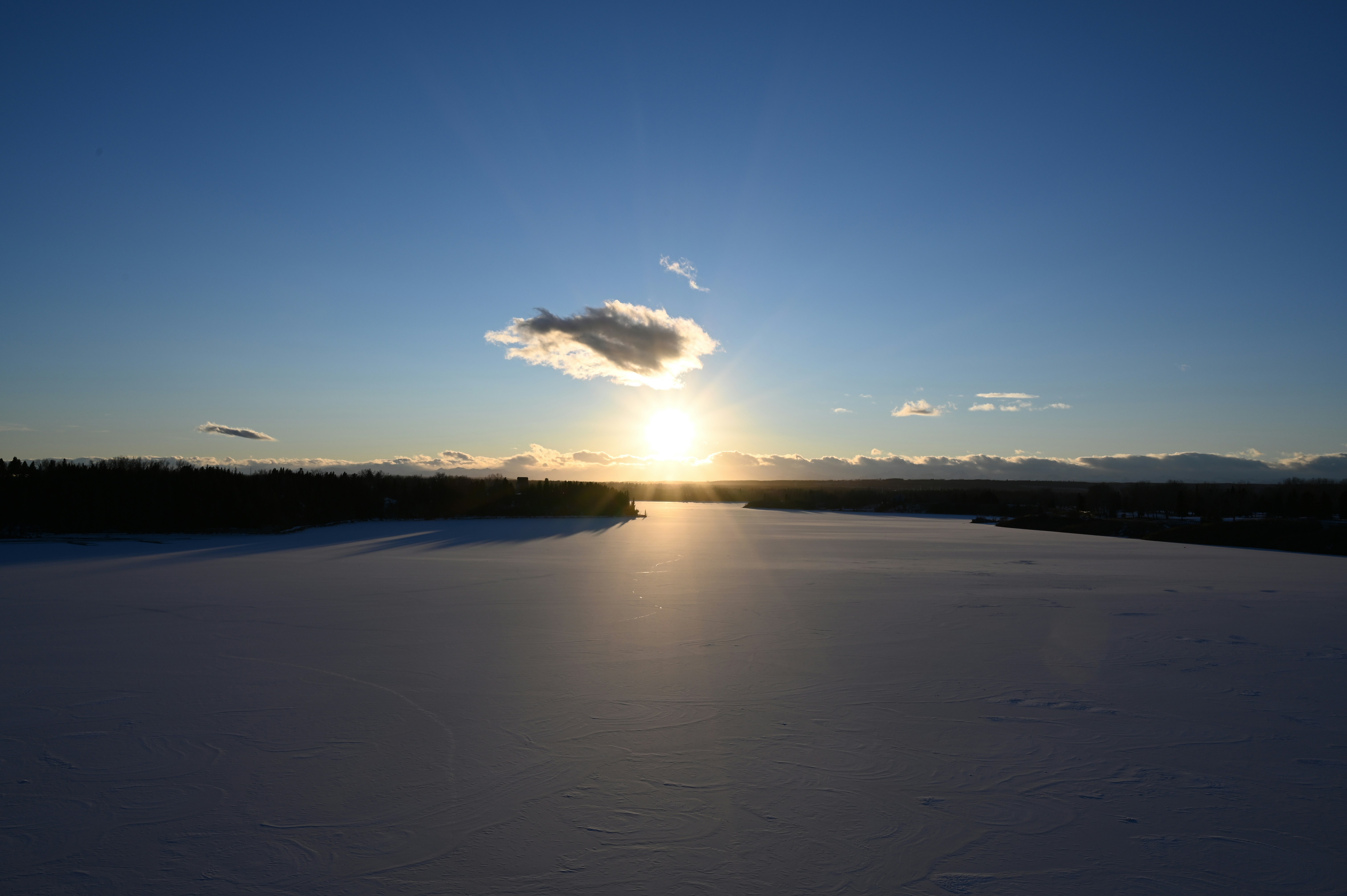 Golden sun setting behind a cloud, casting reflections on a vast, snow-covered landscape.
