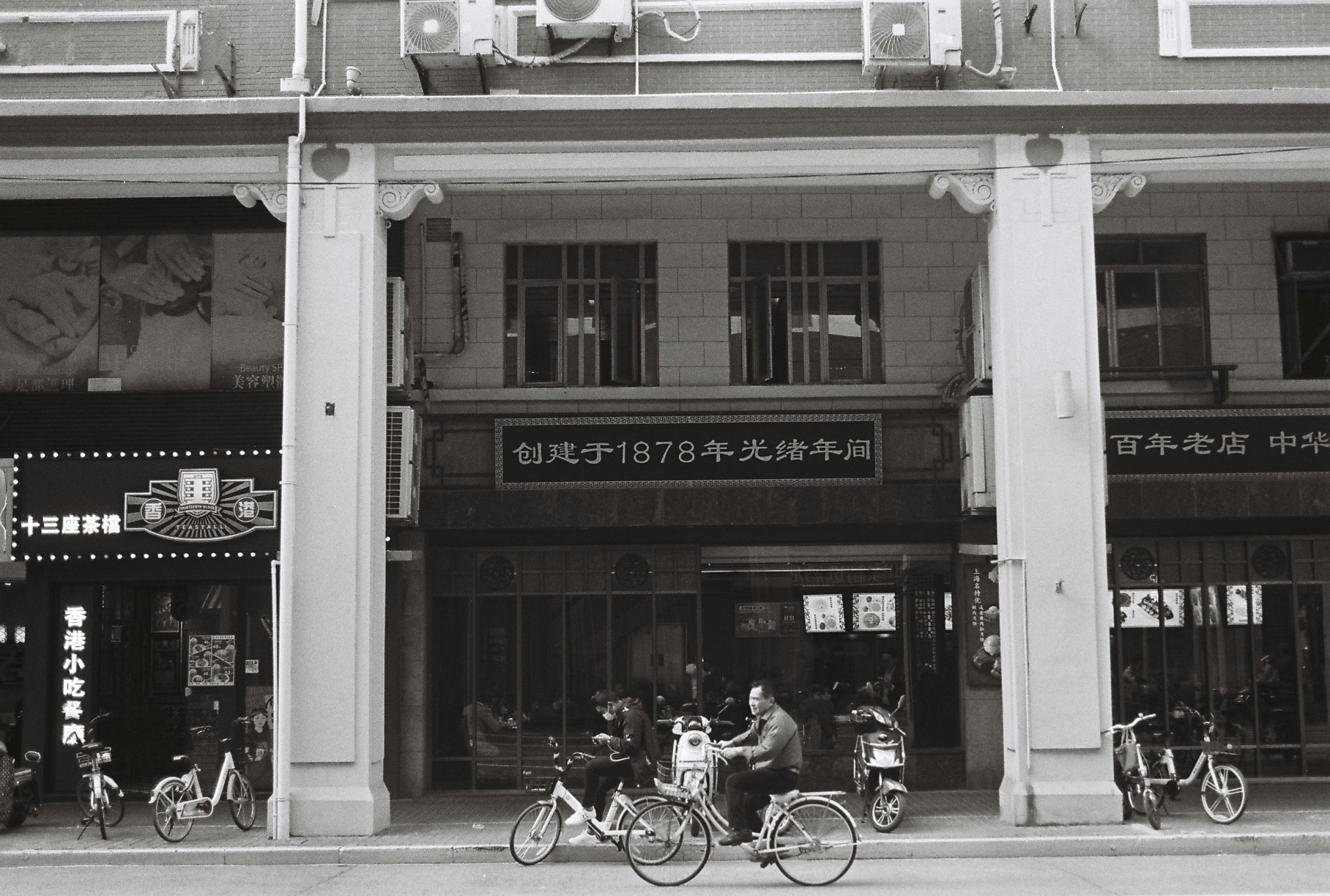 Cyclists pass by a historic building facade in a bustling Shanghai street.