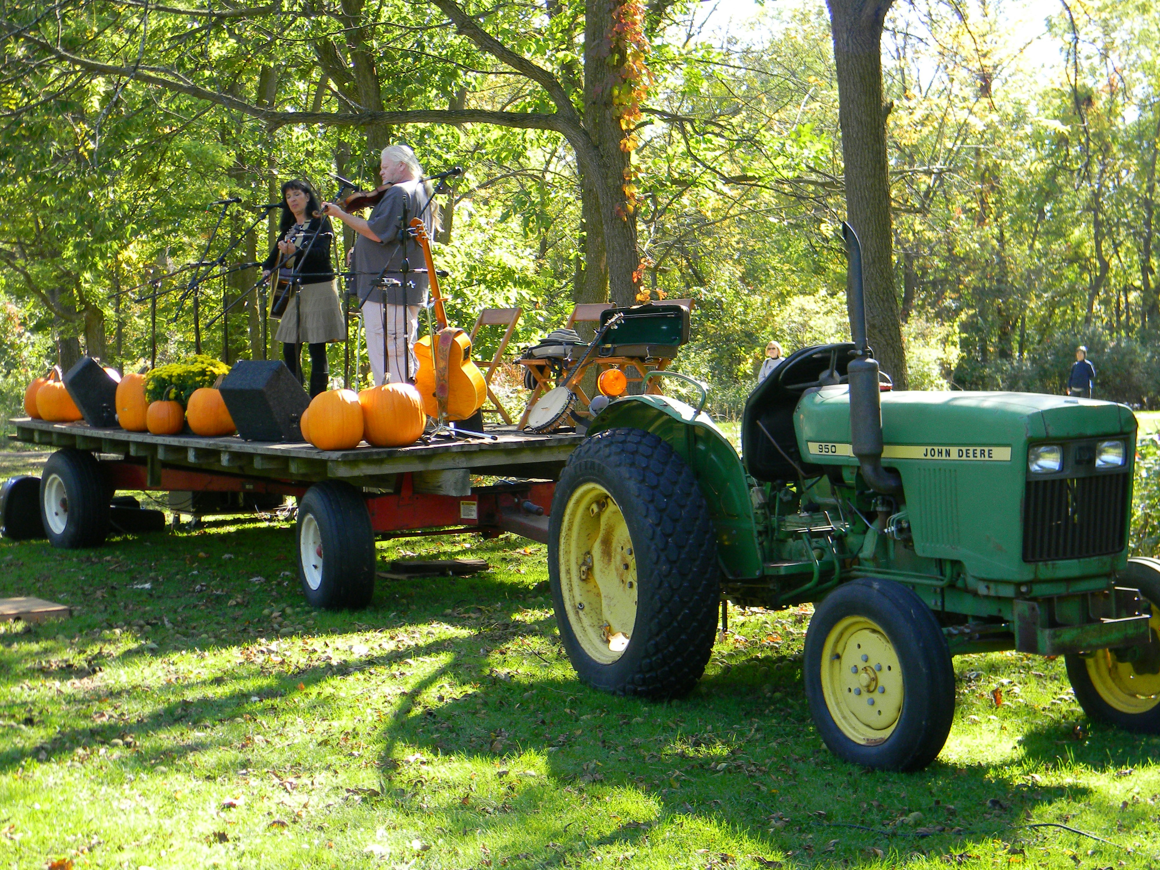 Musicians perform on a trailer adorned with pumpkins, set against a backdrop of vibrant autumn foliage.