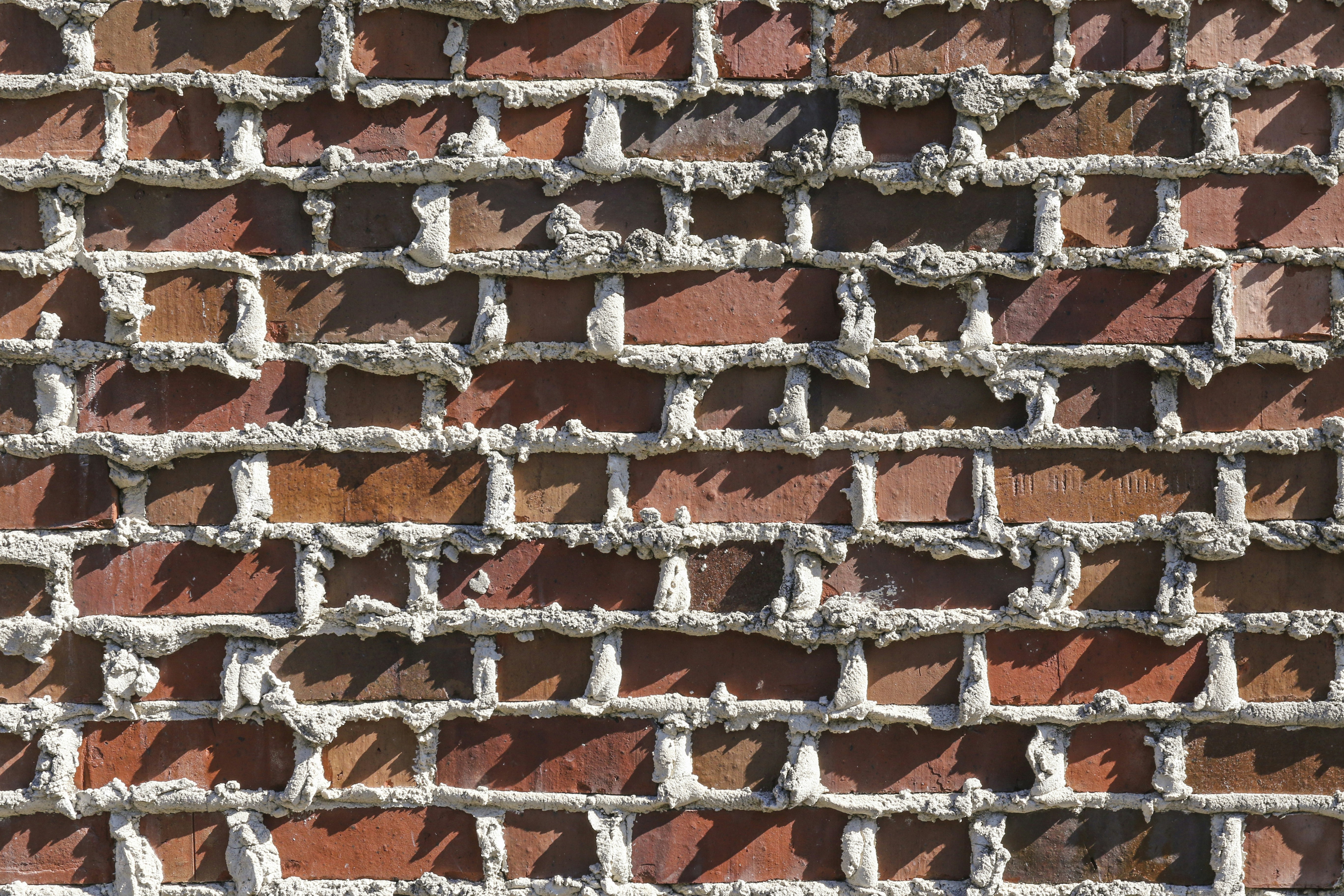Close-up view of a weathered brick wall, showcasing the intricate textures and shadows cast by the uneven mortar. The interplay of light and shadow highlights the wall's character.