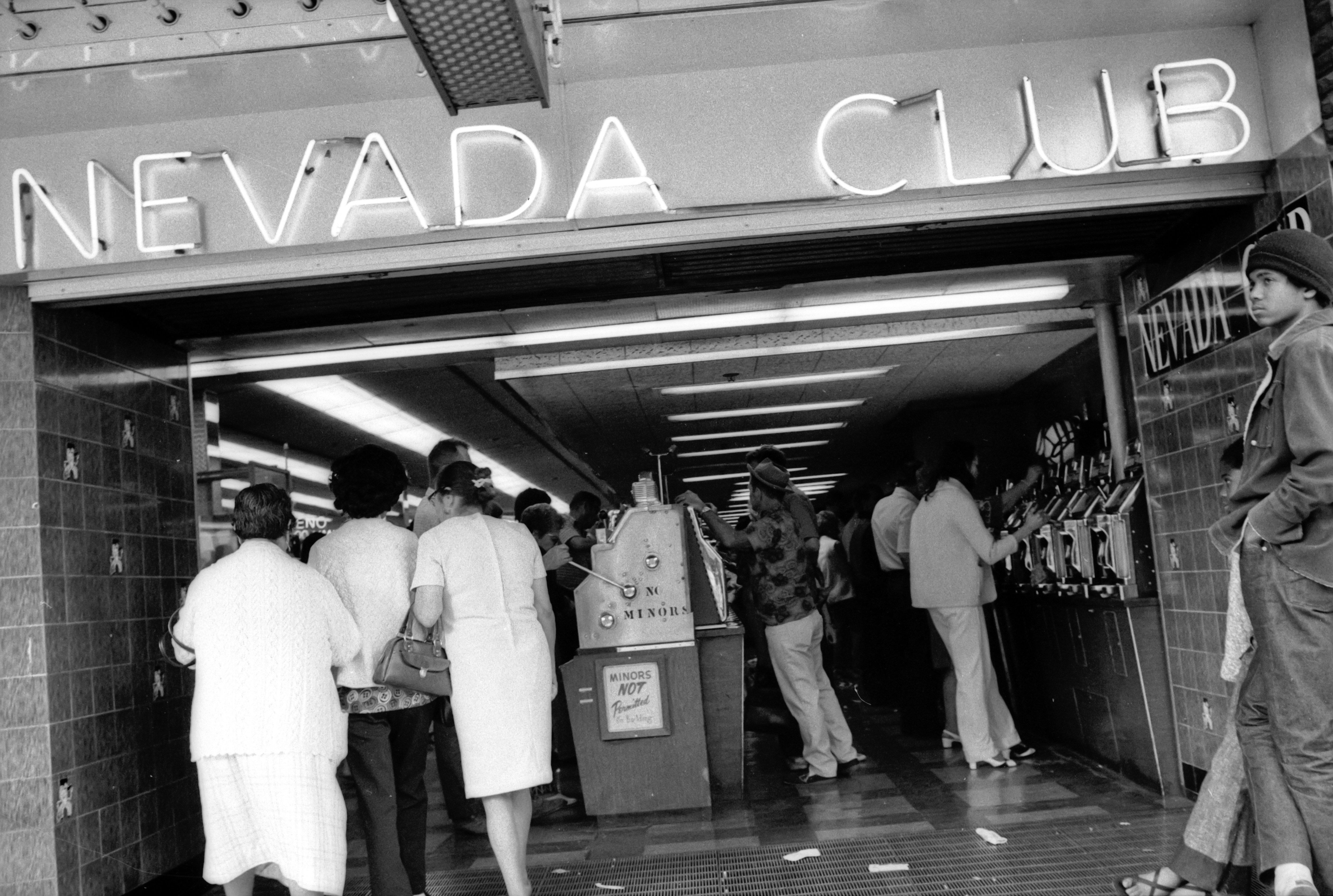 People entering the bustling Nevada Club under neon lights in the 1970s.