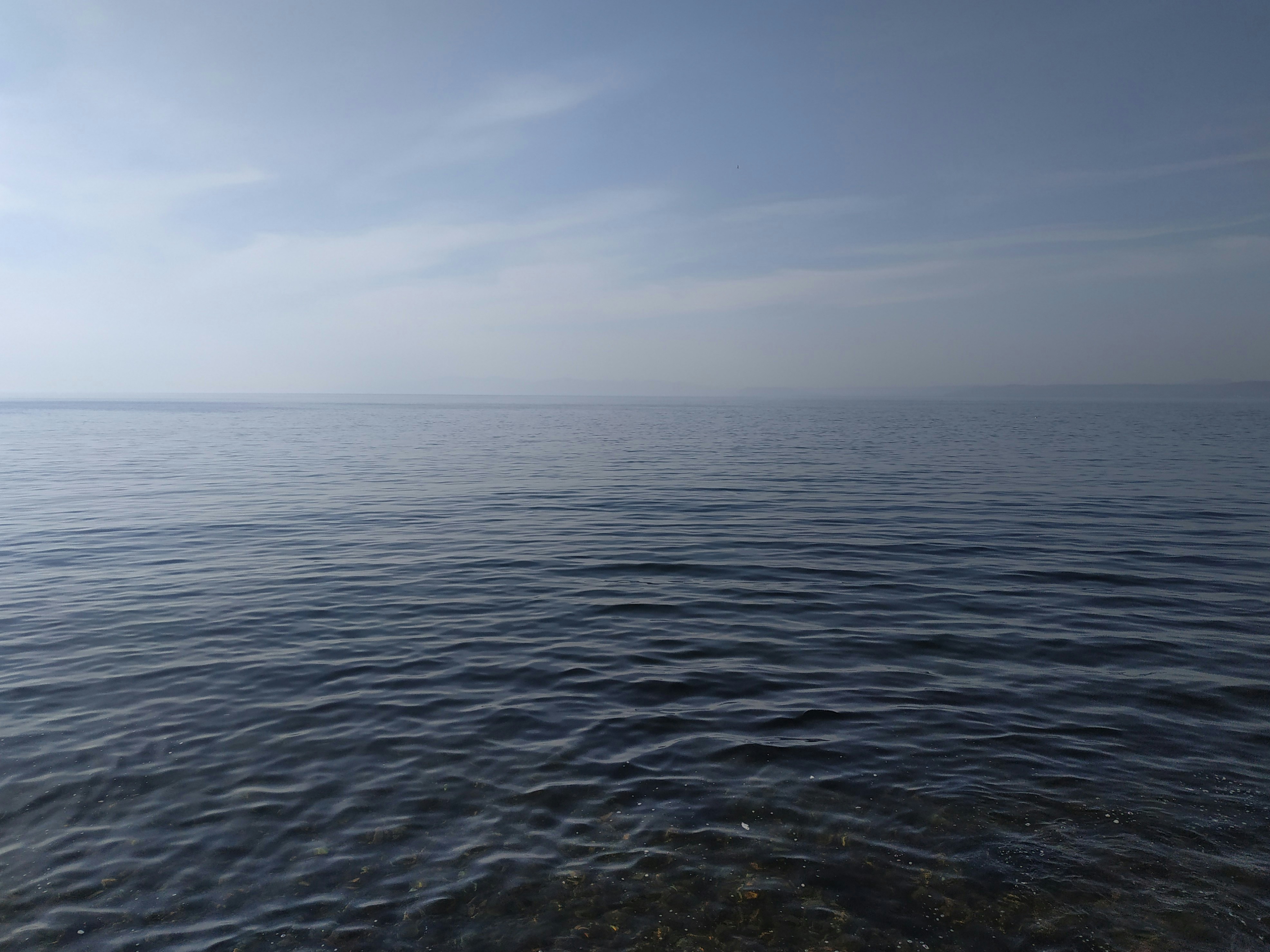 Vast expanse of calm sea meeting the soft blue sky at a distant horizon.