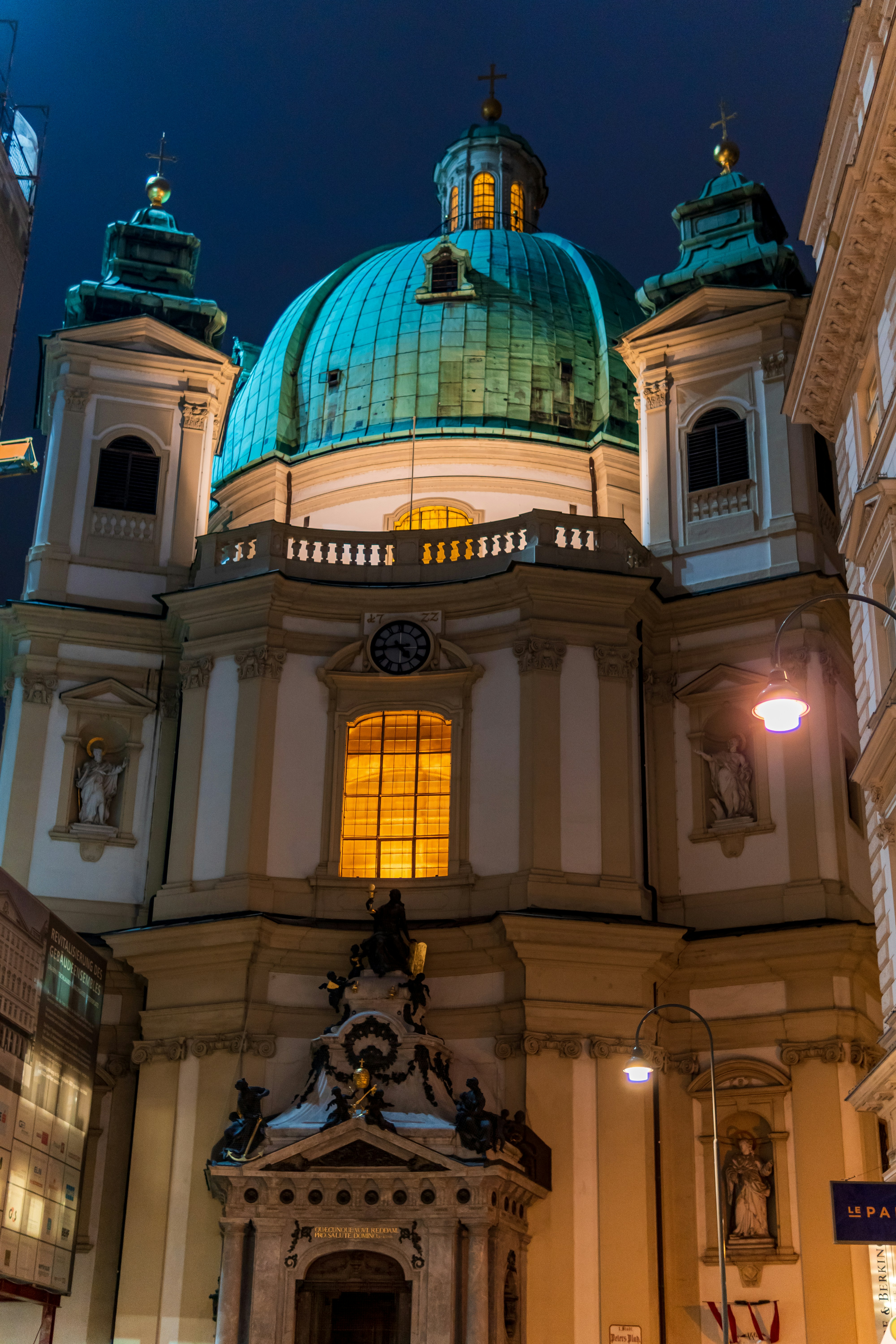 Baroque church facade featuring a striking green dome and illuminated windows against a night sky.