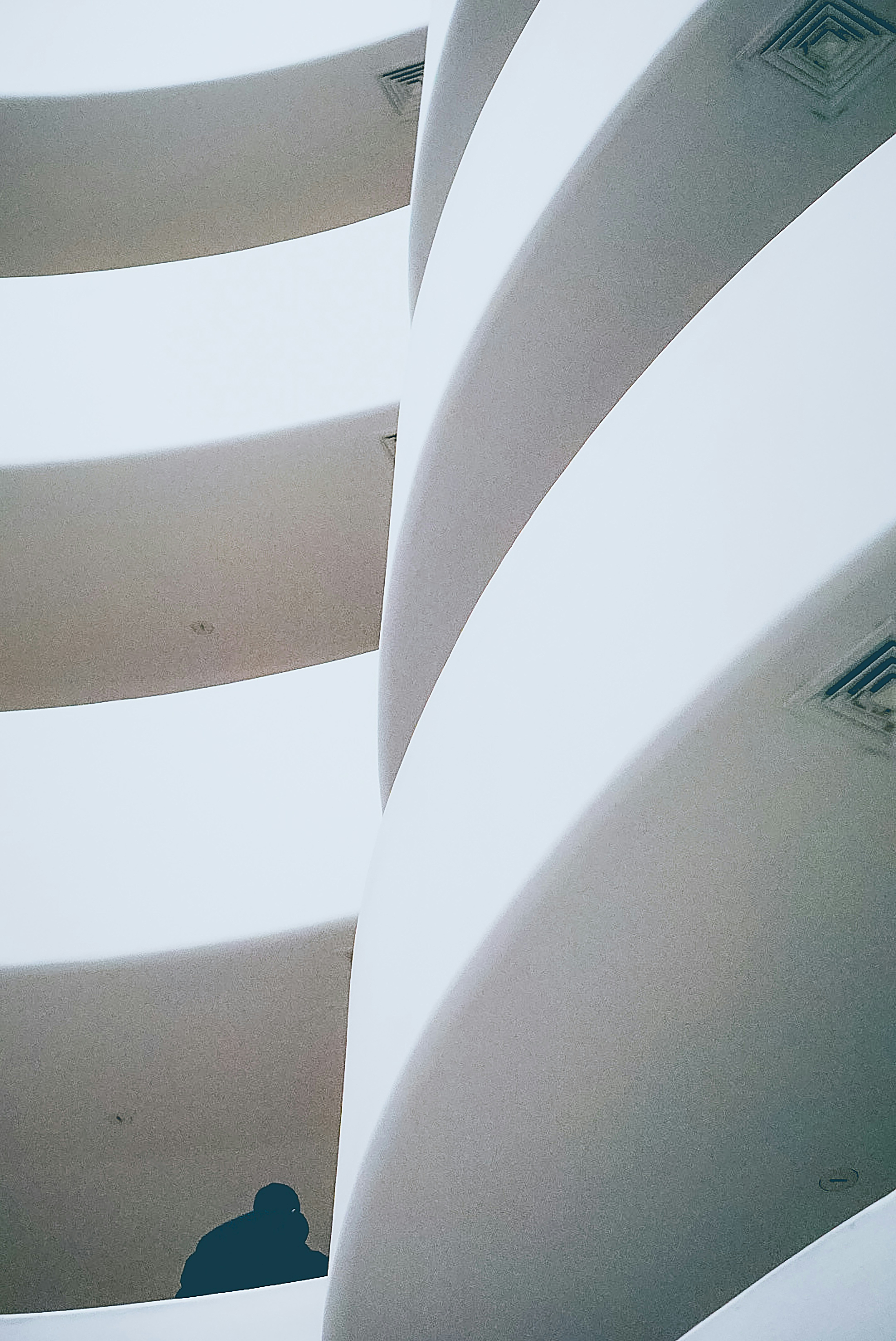 A person stands on a spiraling staircase, surrounded by smooth, white walls that create a sense of movement and depth.
