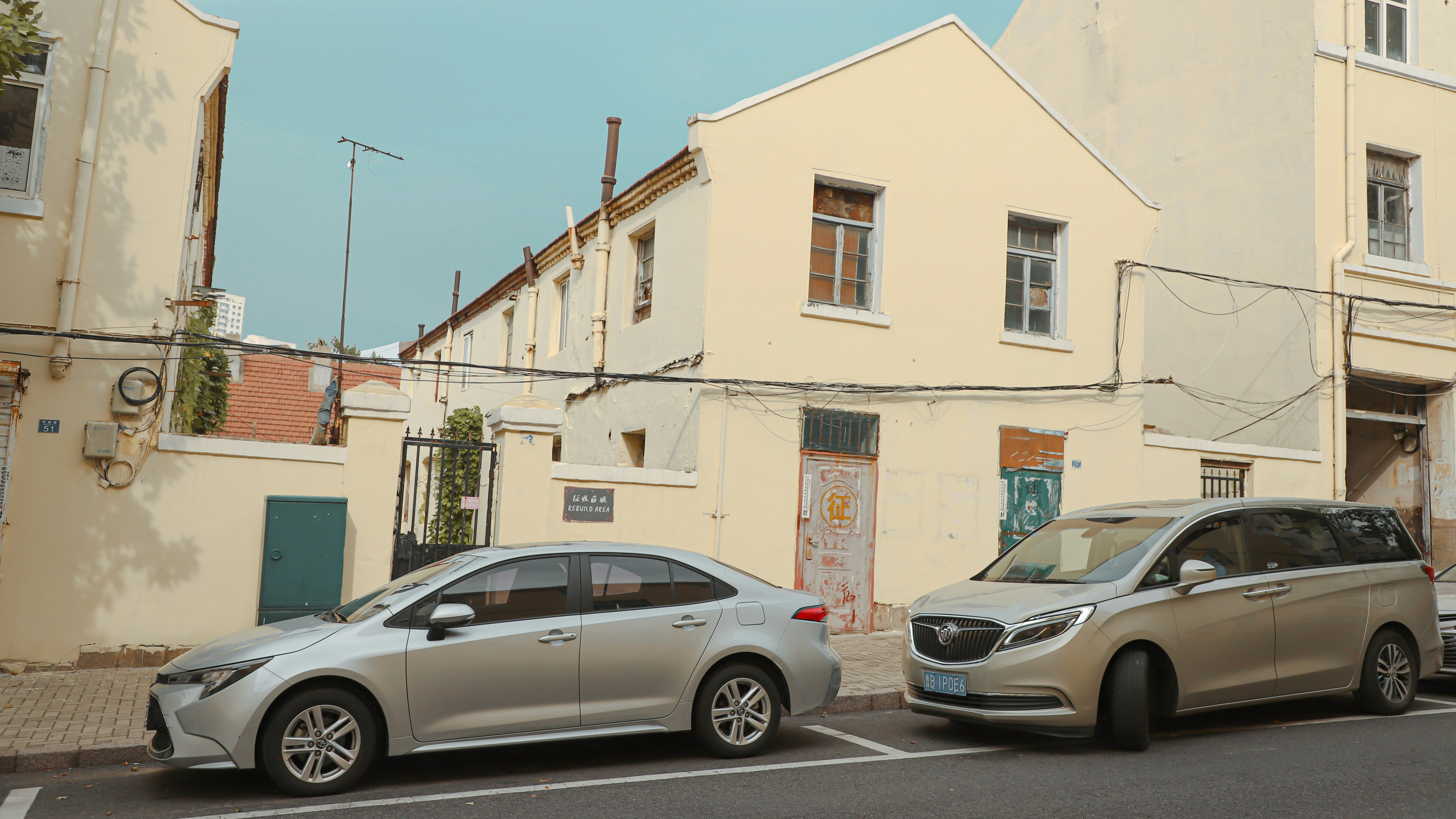 Two cars parked along a quiet street lined with cream-colored buildings under a clear sky.