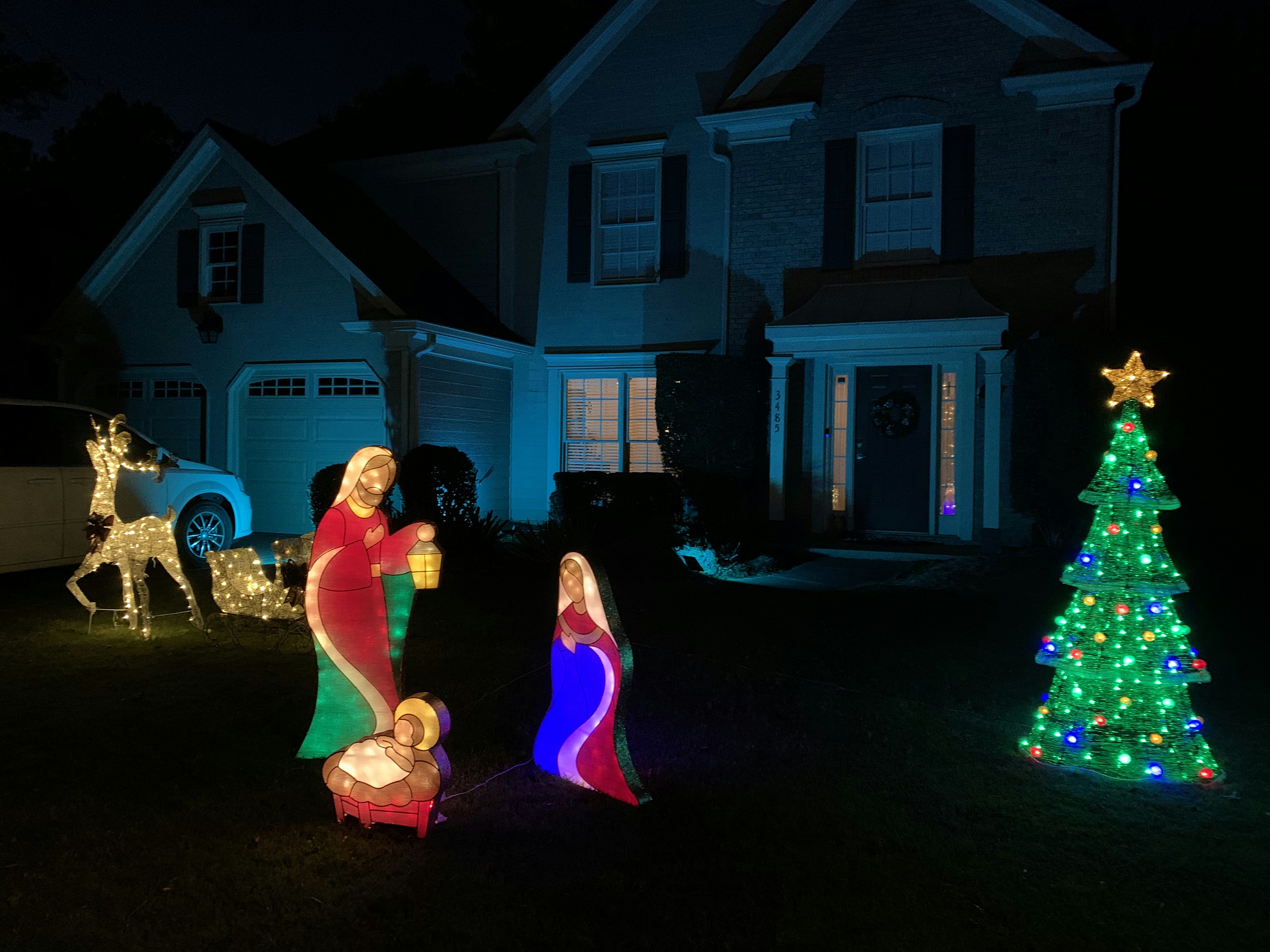 Lantern-lit Nativity under Neon Christmas Tree Lights in a Suburban Yard