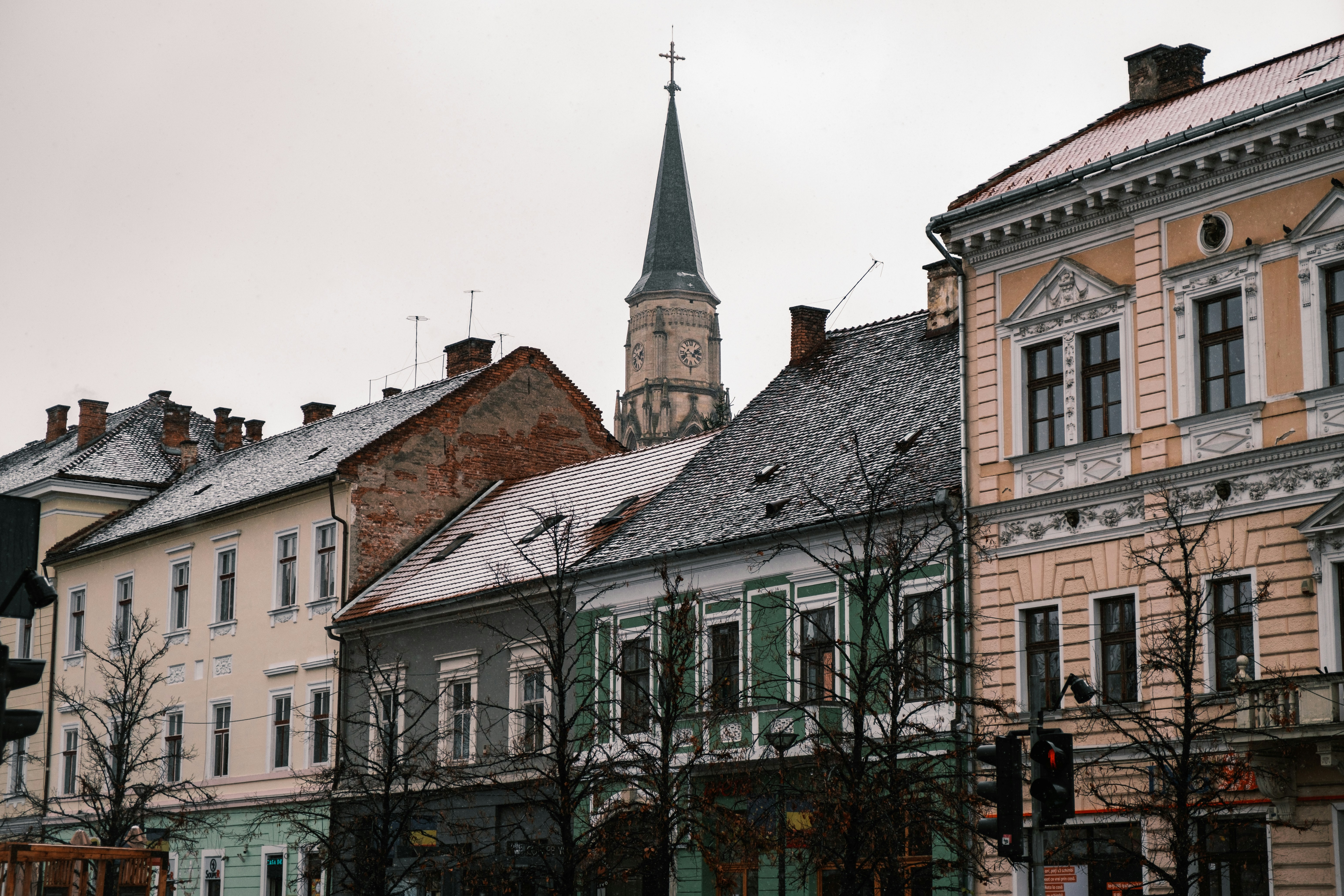 Snow-dusted historic buildings with a church spire rising in the background under a cloudy sky.