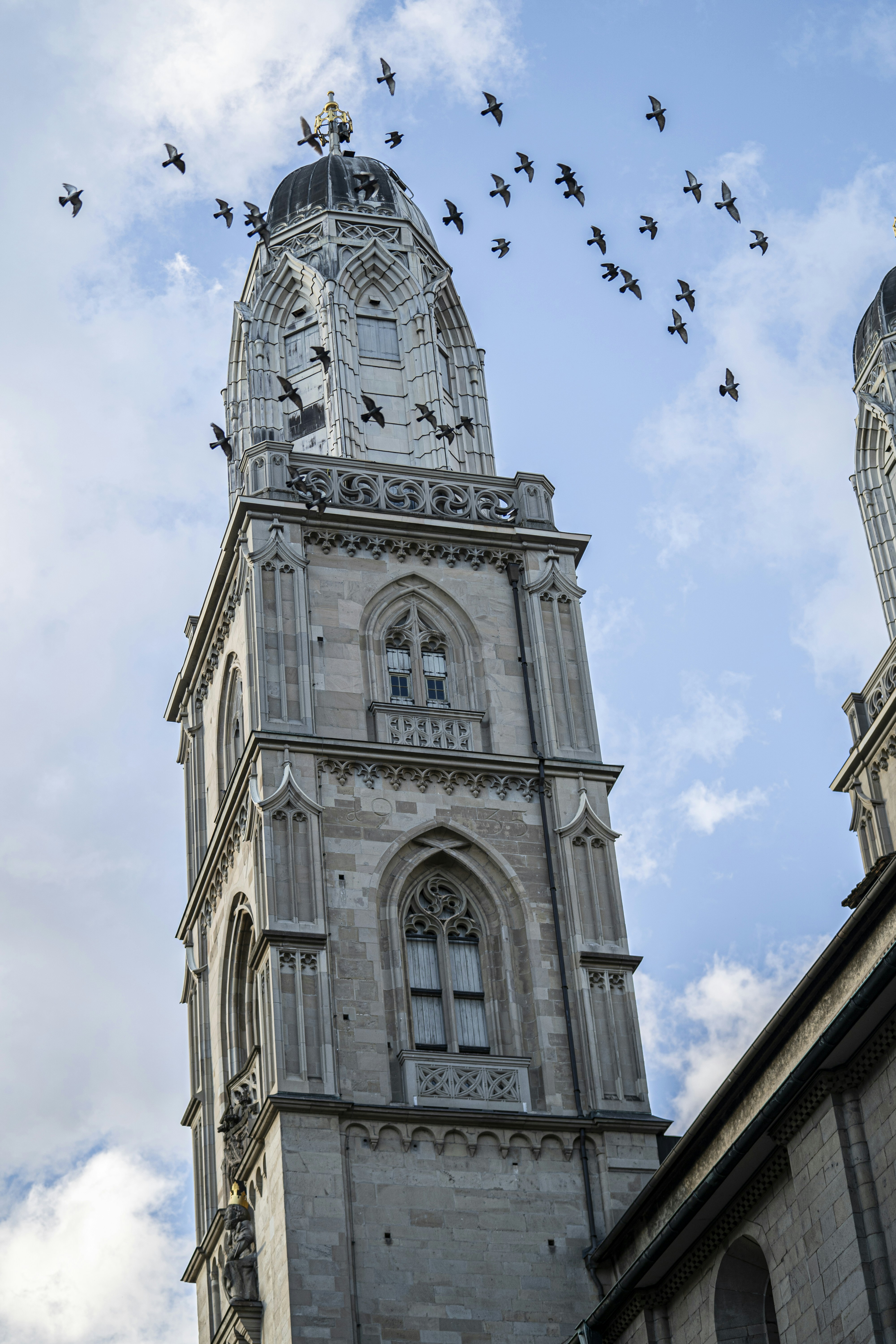 Flock of birds soaring near the towering spires of a historic church against a cloudy sky.