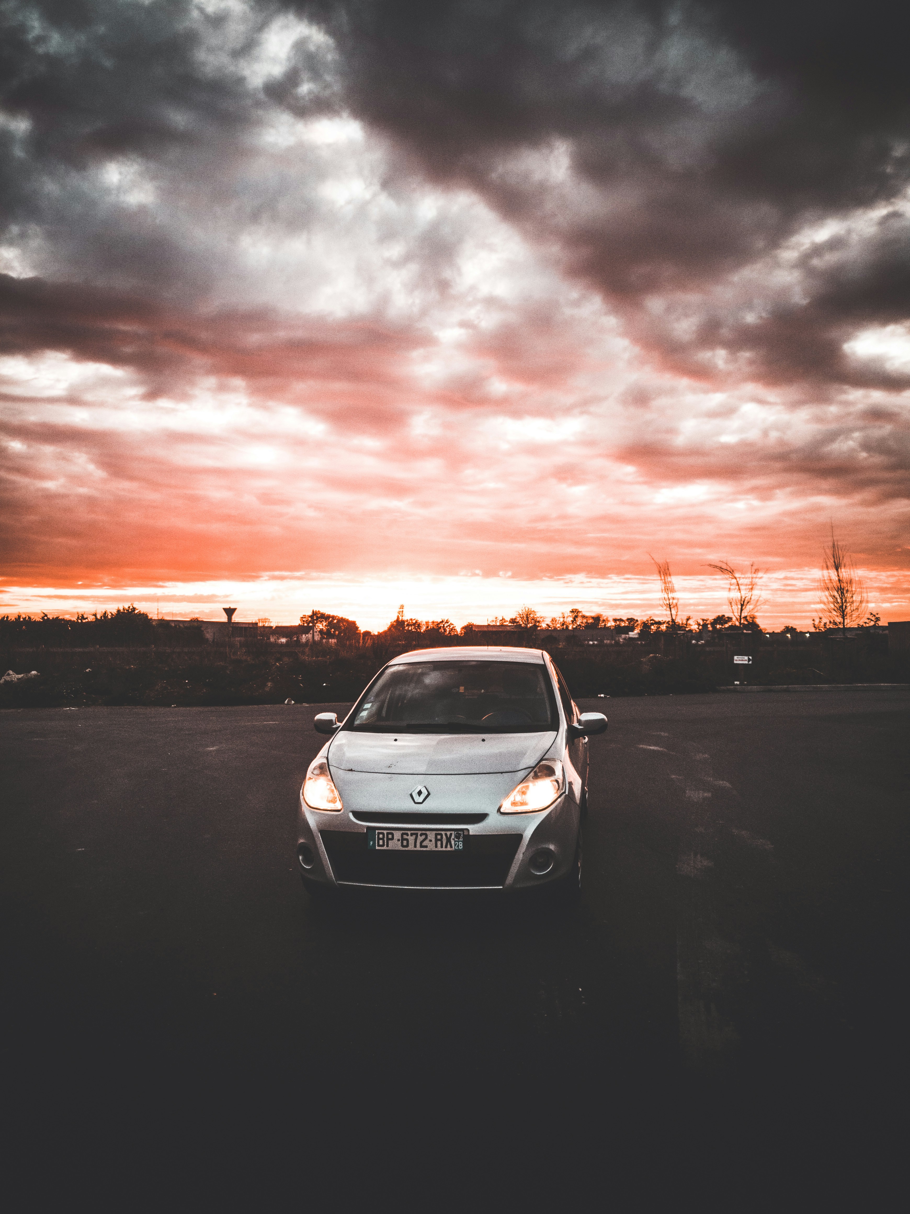 Dusk Chiaroscuro: Silver Hatchback Beneath a Fiery Sky