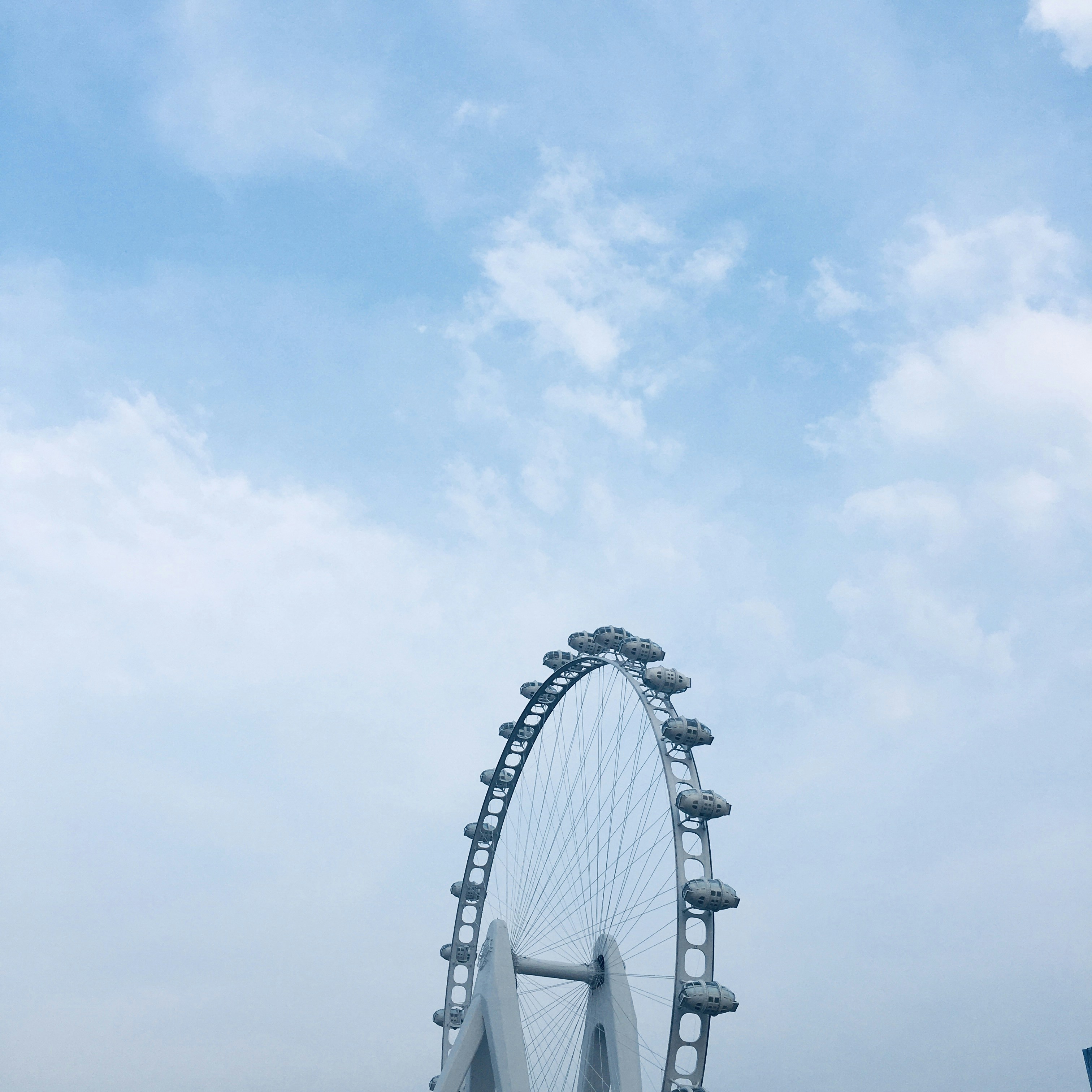 A Ferris wheel stands tall against a backdrop of soft clouds and blue sky, inviting visitors to experience the thrill of heights.