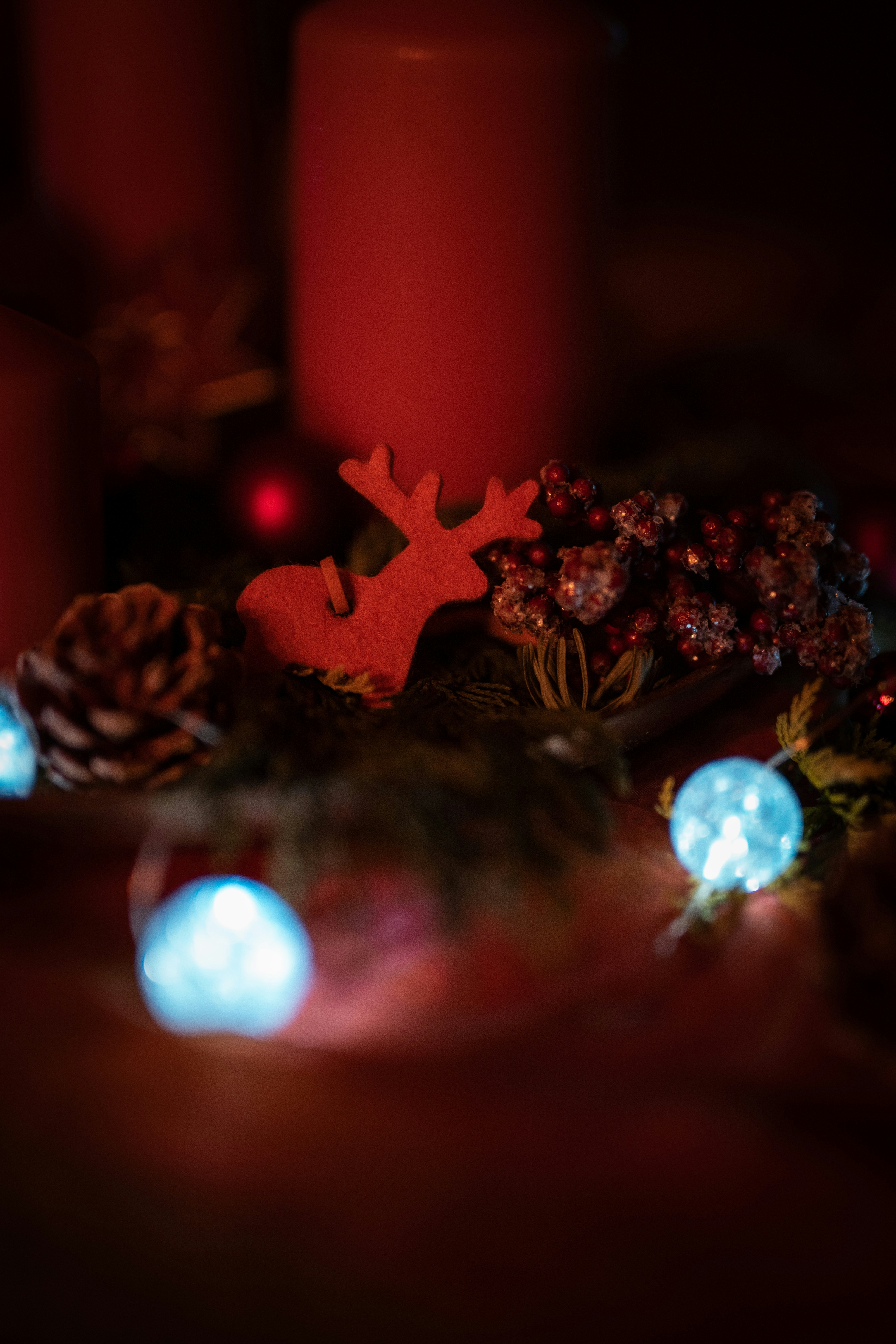 A playful red reindeer ornament nestled among pinecones and colorful lights, evoking a cozy holiday atmosphere.