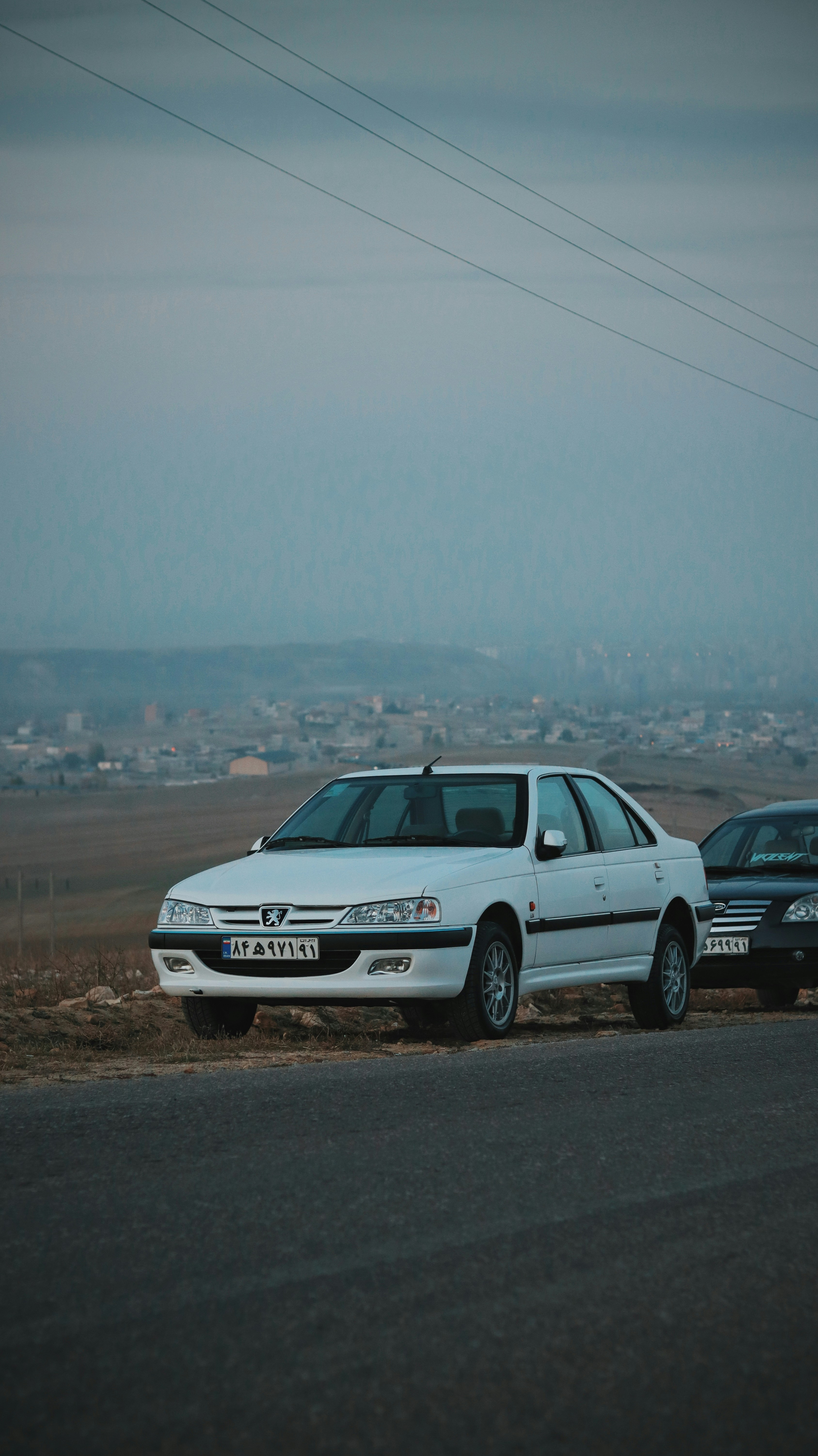 White Sedan at the Edge: Quiet Desert Road Beneath Overhead Power Lines