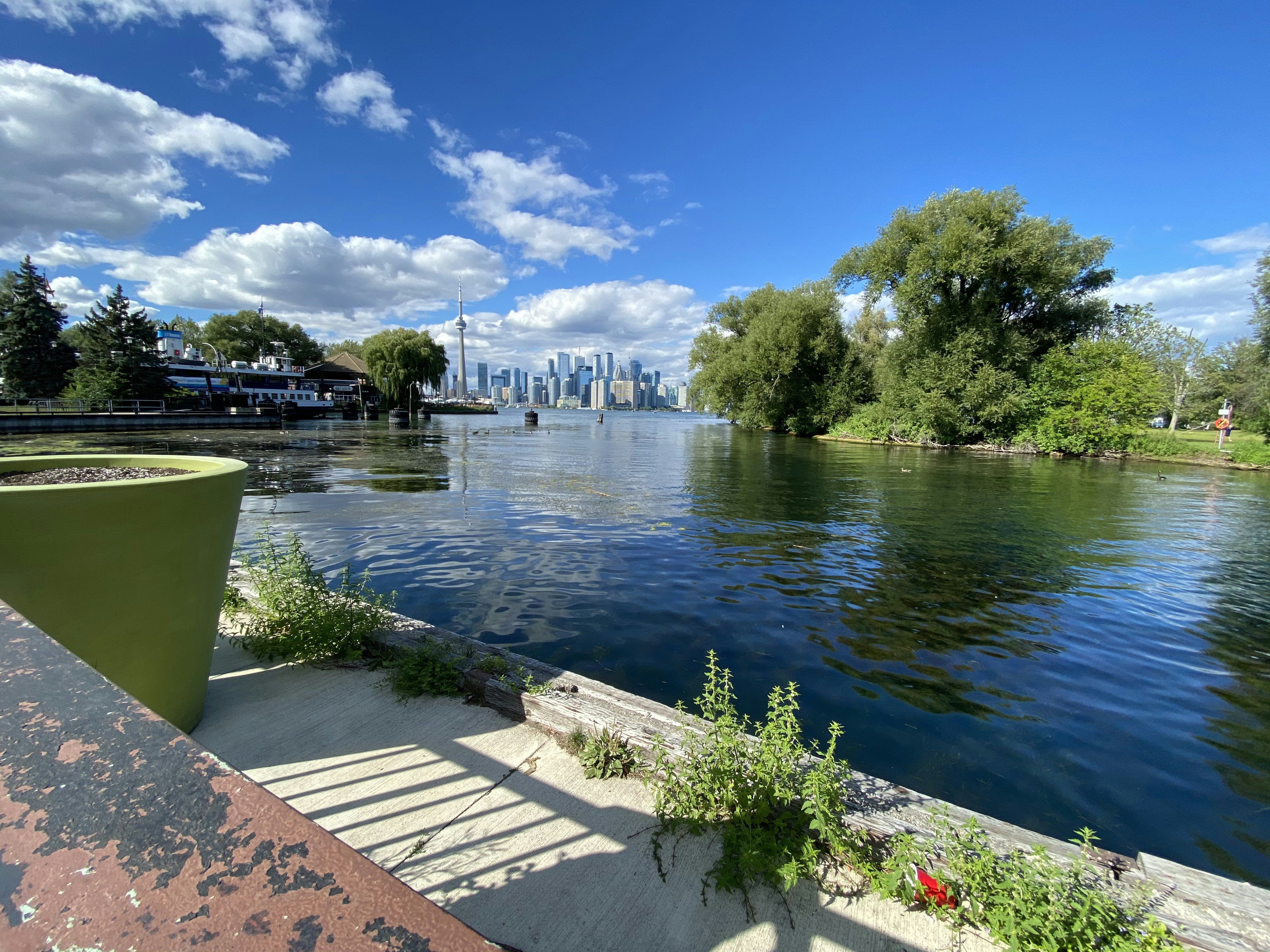Riverside view with city skyline under a vibrant blue sky and scattered clouds.