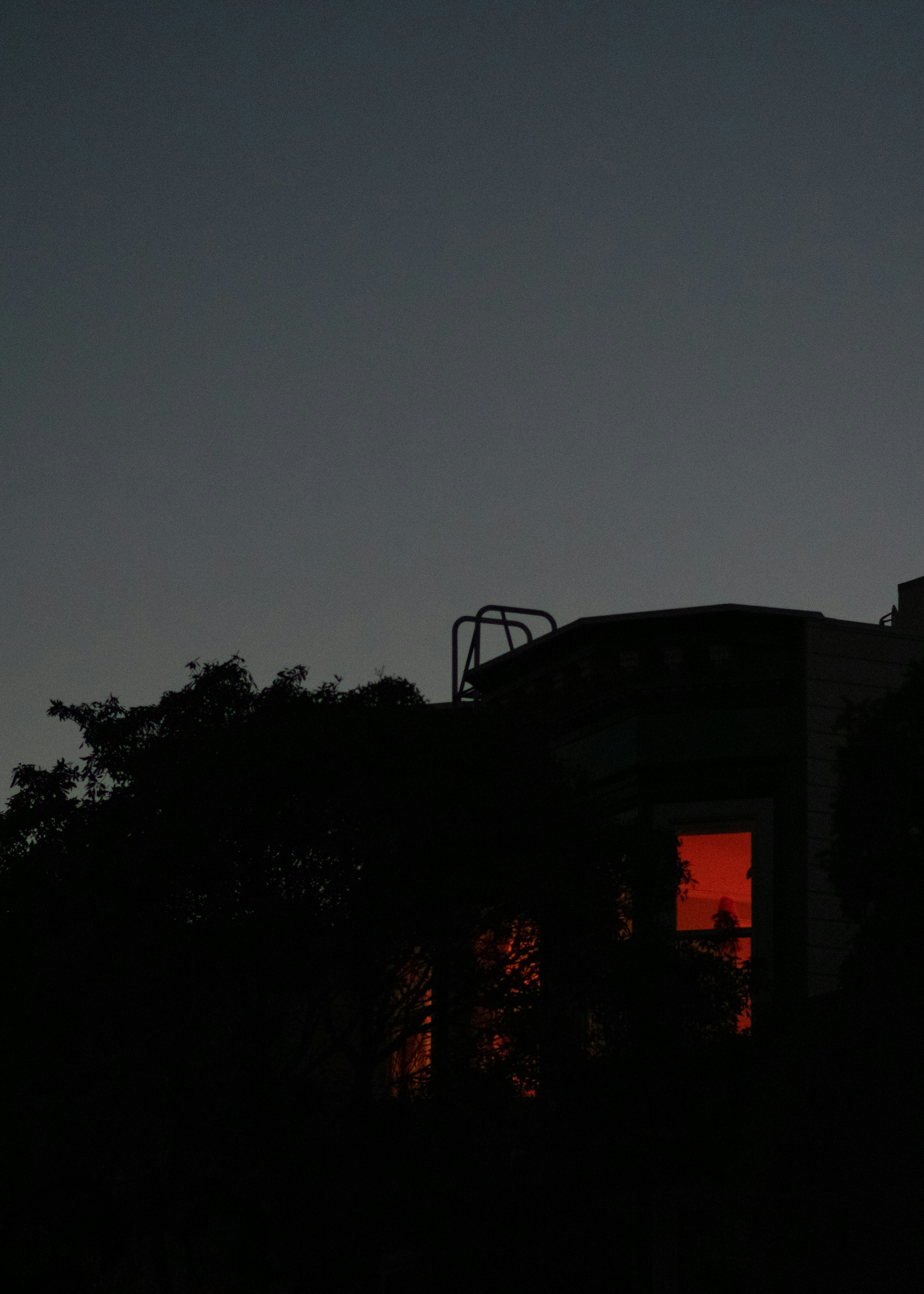 Silhouette of a building against a twilight sky, with a vivid orange glow emanating from a window. The scene captures the transition from day to night.