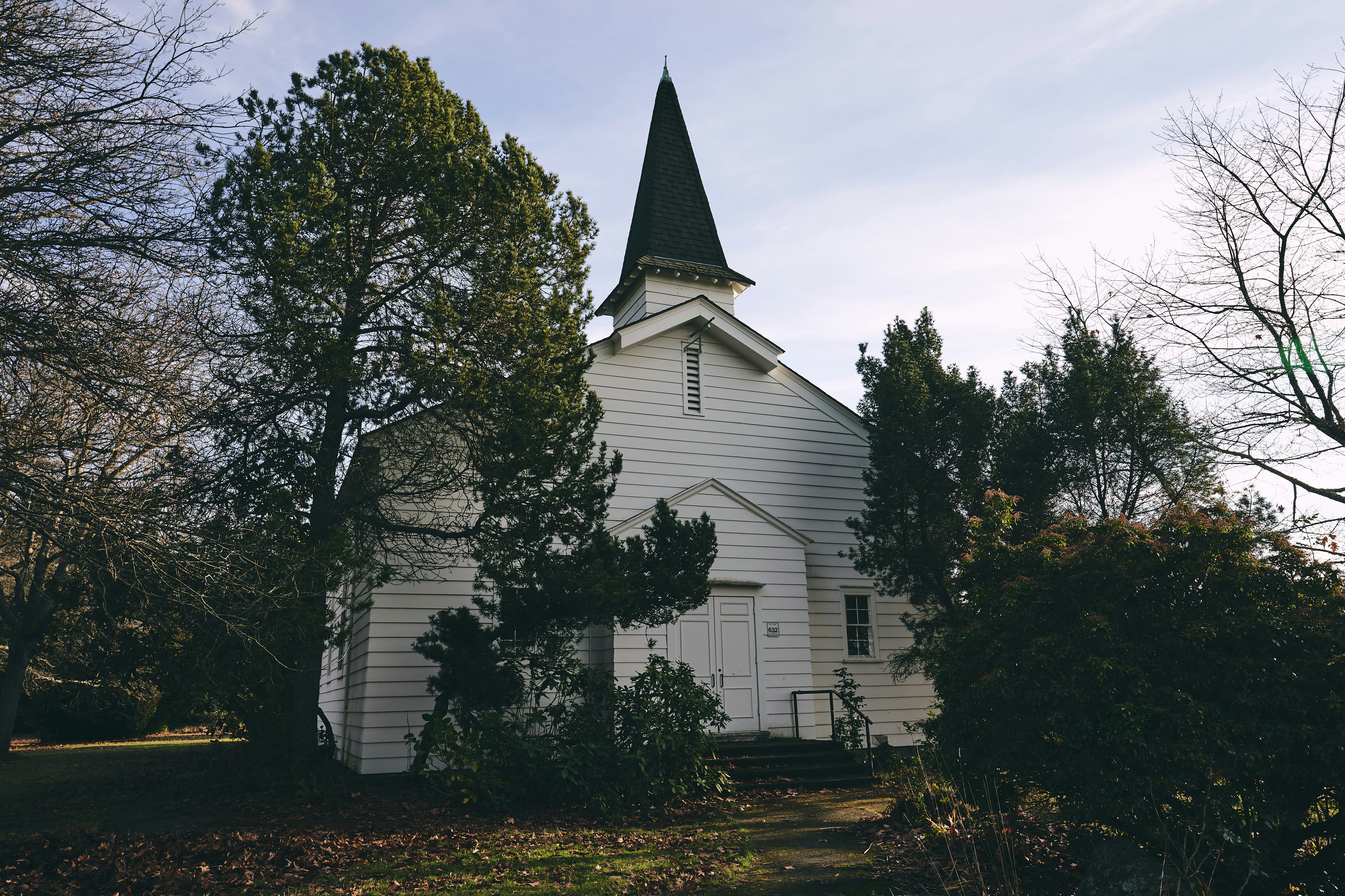 A quaint white chapel nestled among trees, showcasing its tall spire and inviting entrance. The scene evokes a sense of tranquility and nostalgia.