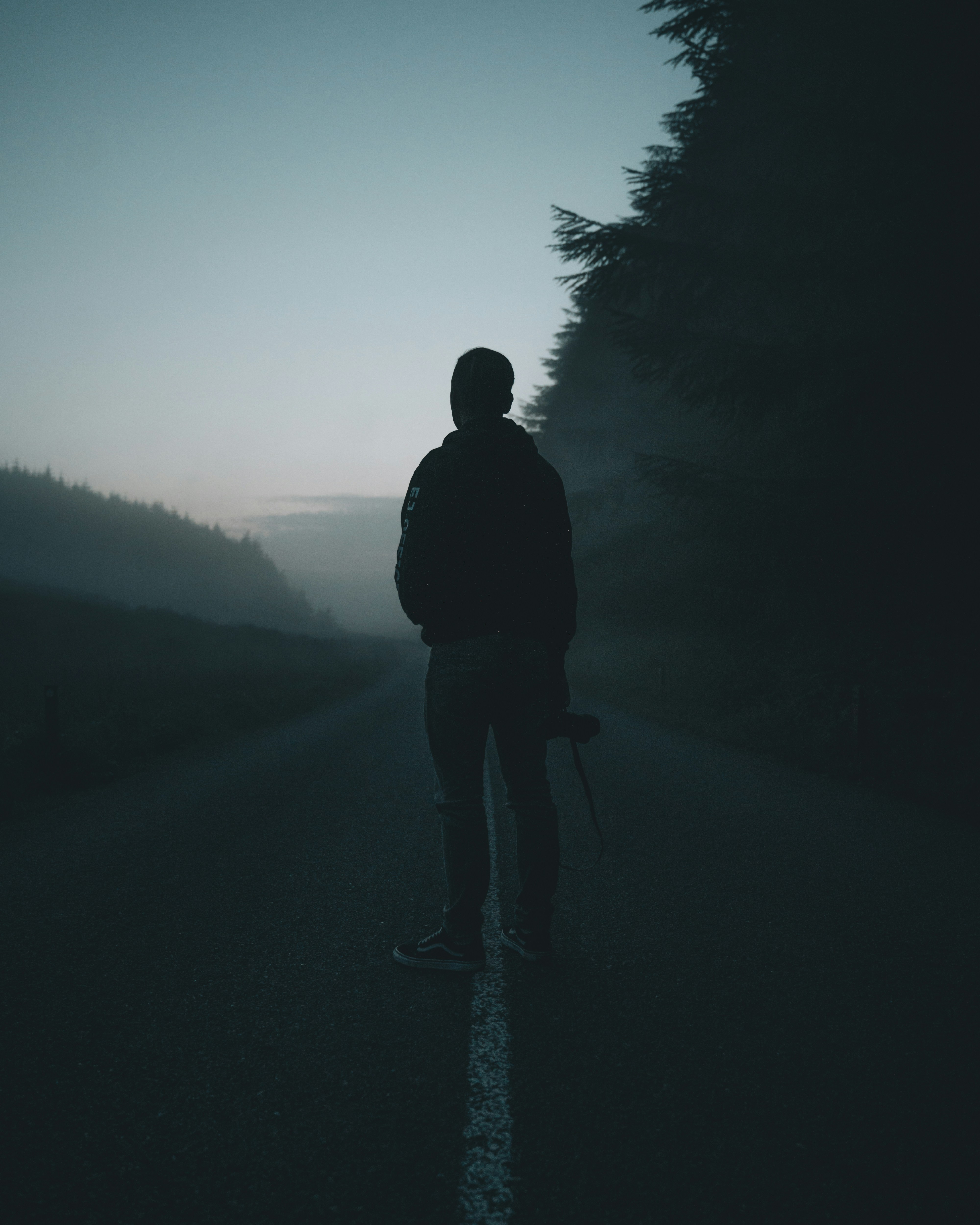 Silhouette of a person standing on a deserted road surrounded by a misty landscape at dawn.