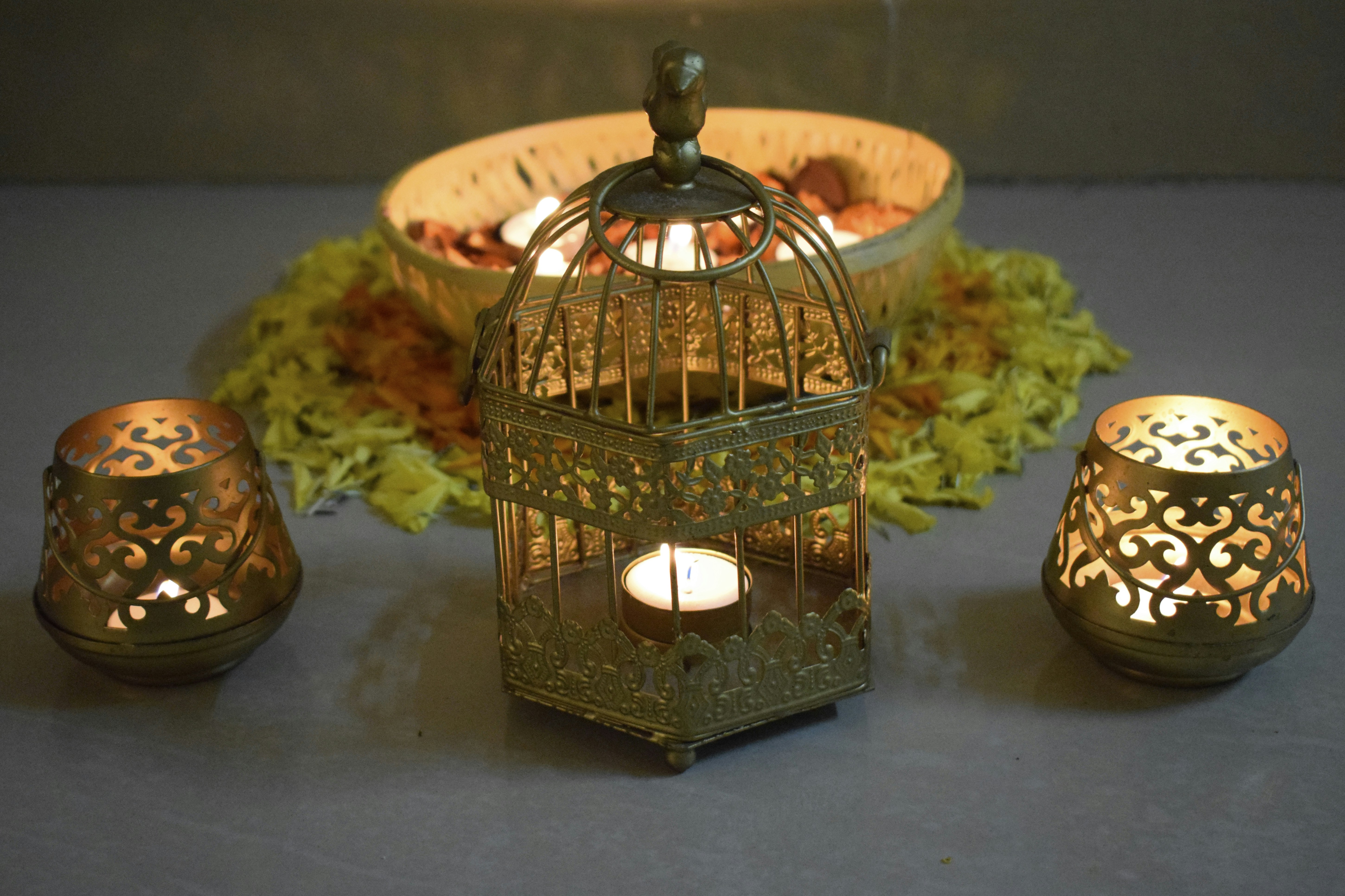 Decorative lantern surrounded by candles and a bowl of petals on a soft surface, creating a warm ambiance.
