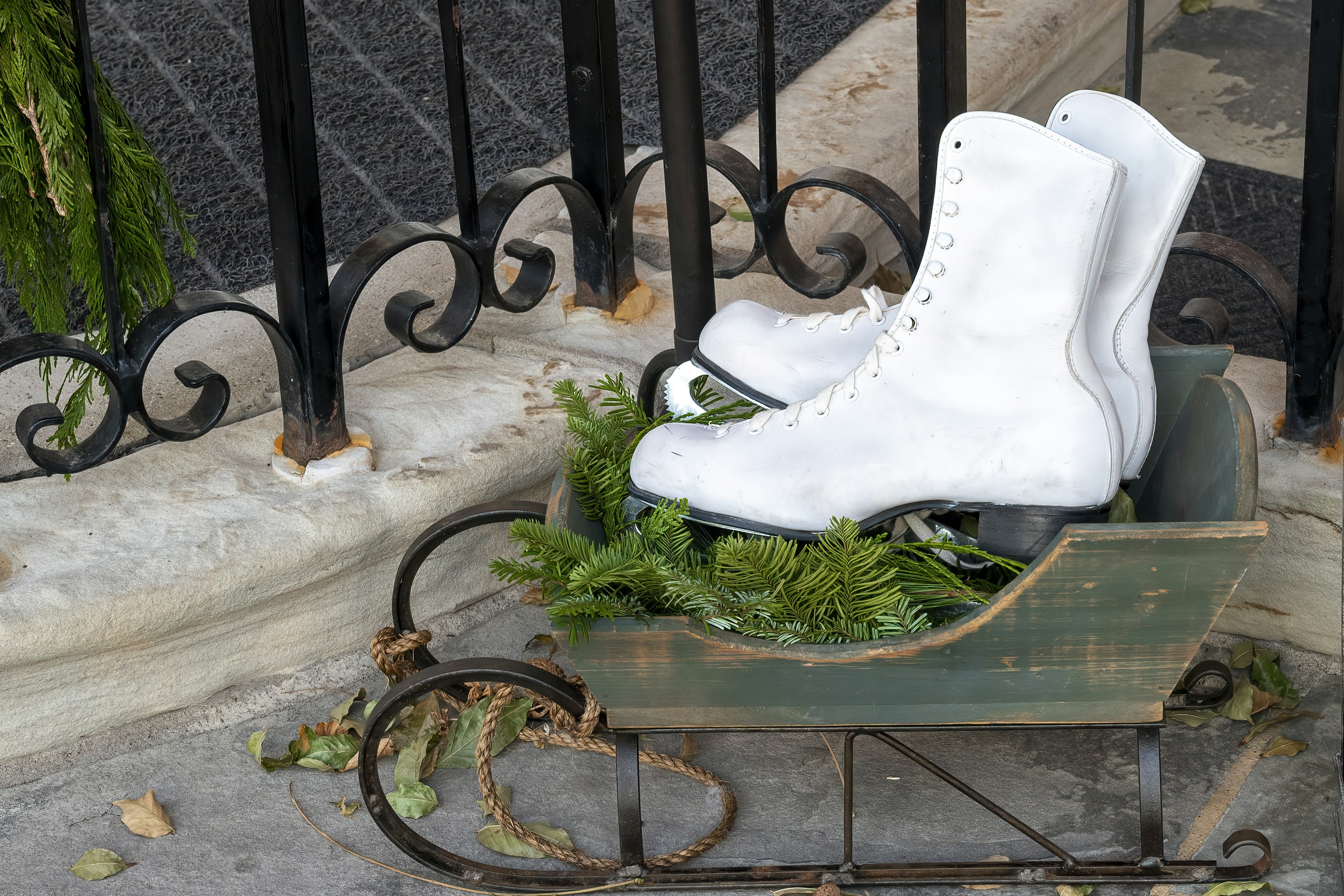 White Ice Skates Rest on a Weathered Green Sled Beside Wrought-Iron Rails