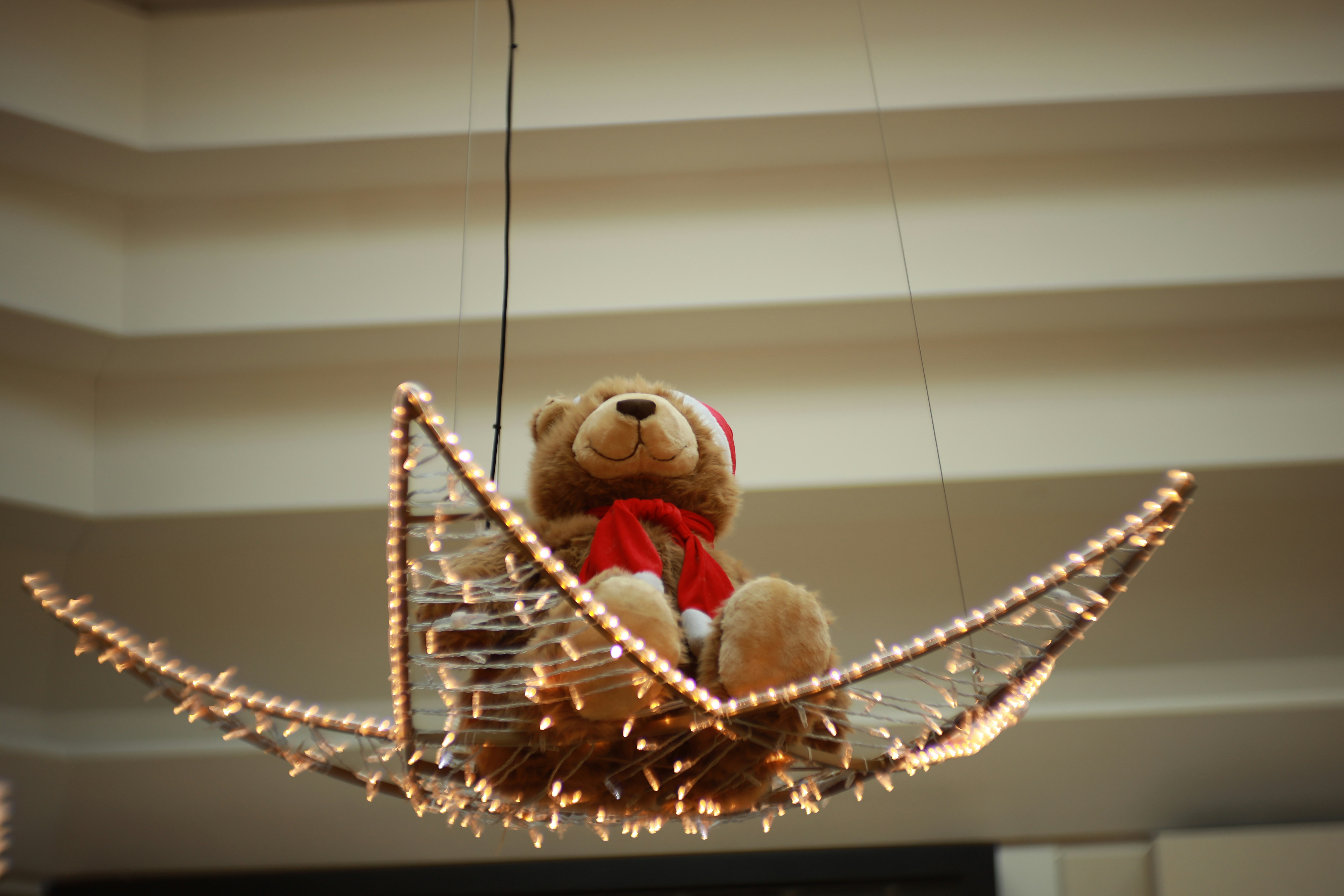 A plush bear wearing a red scarf sits atop a creatively designed lighted structure, adding a playful touch to the festive decor.