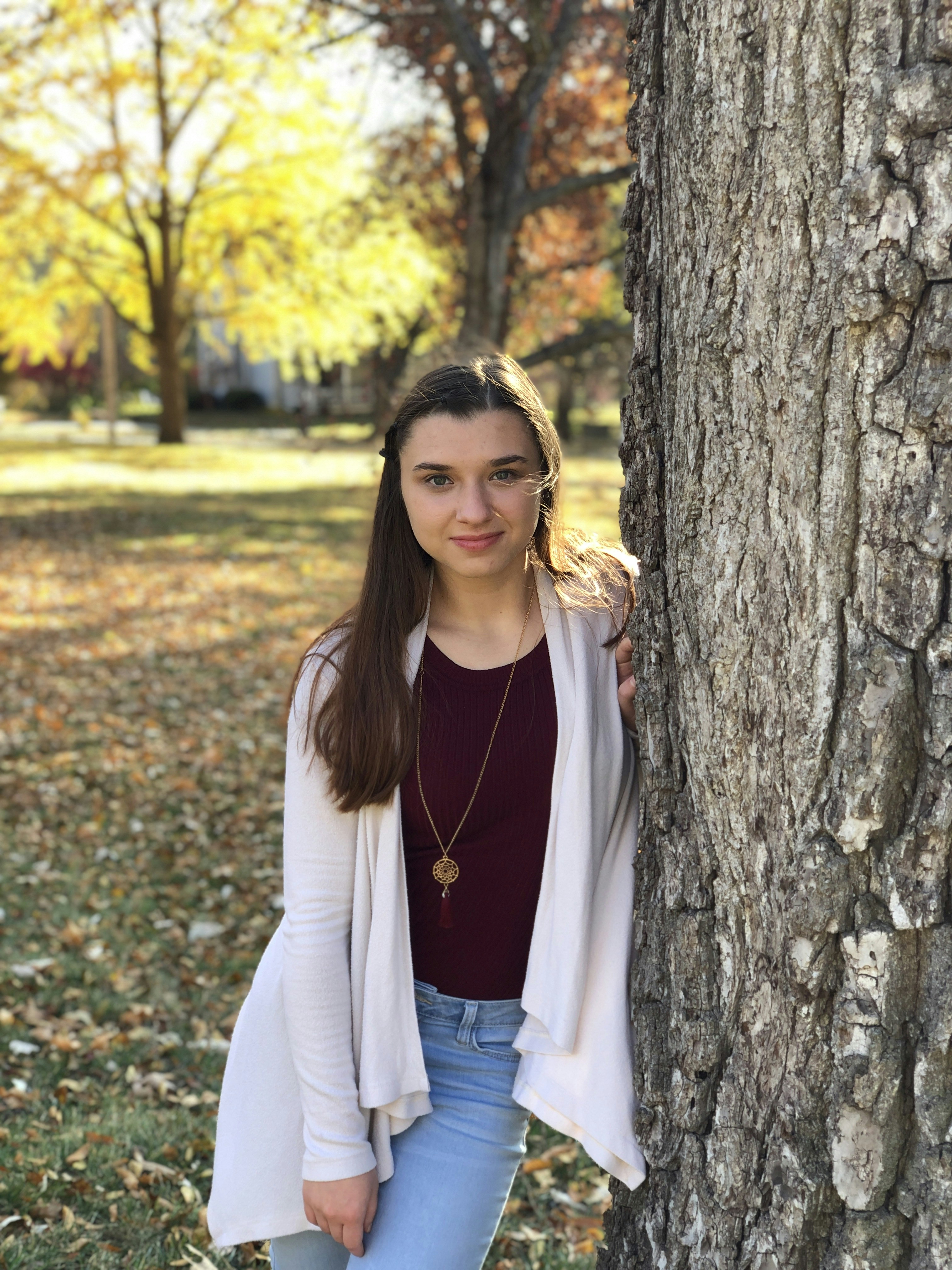 woman in white cardigan standing beside brown tree during daytime