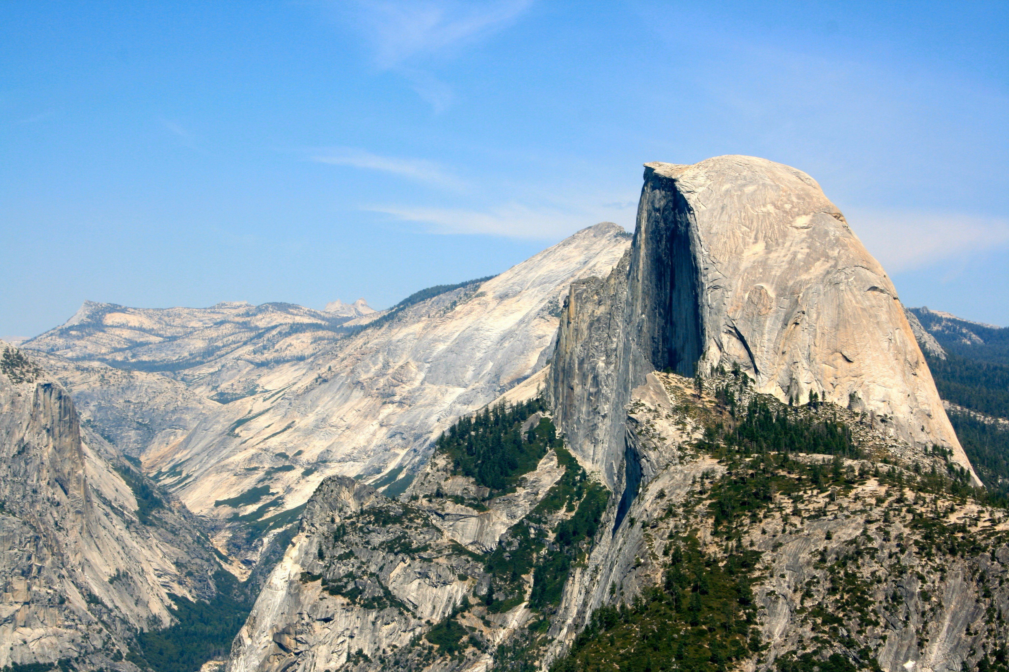 Half Dome rises majestically above the rugged landscape of Yosemite National Park, surrounded by rolling hills and distant peaks.