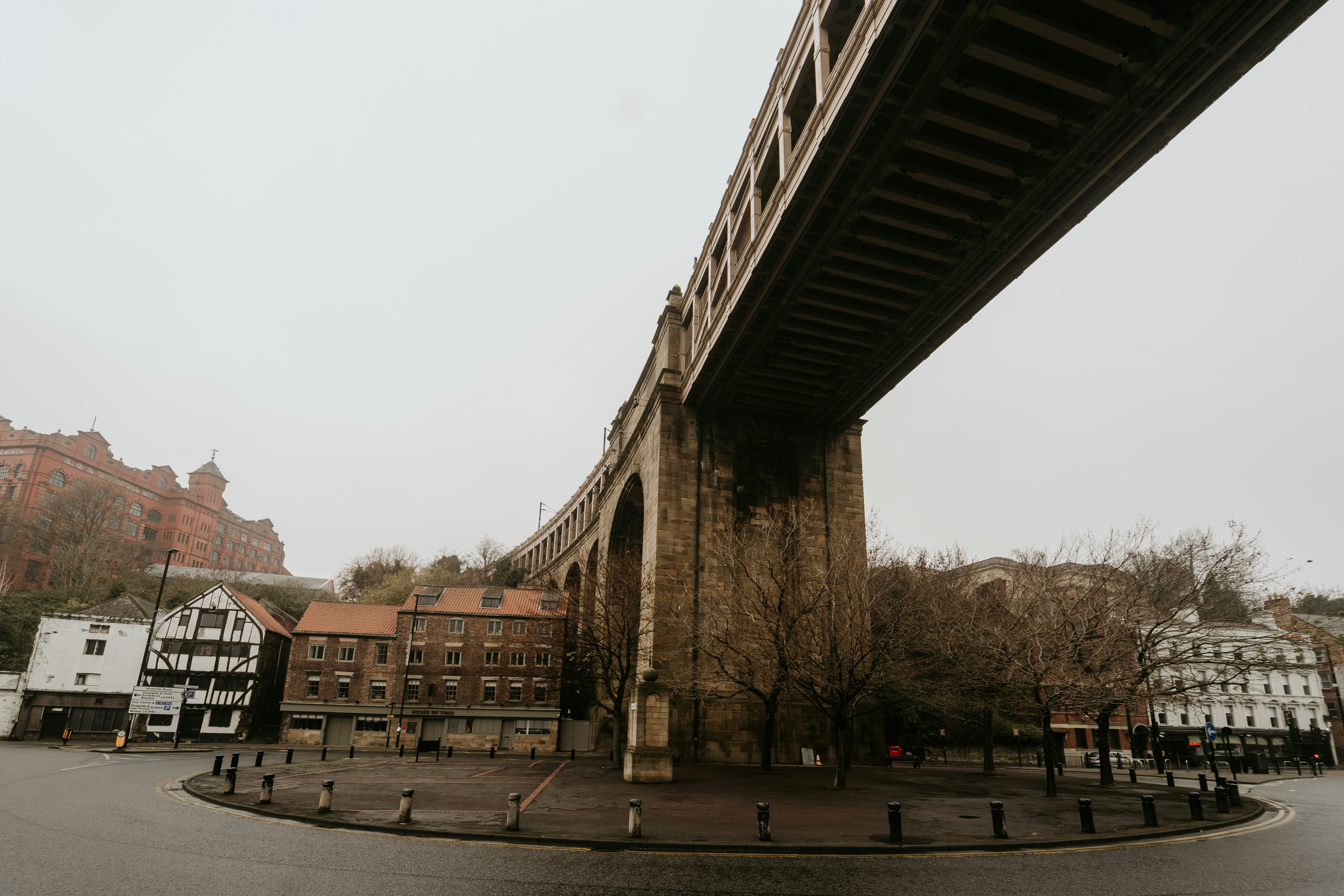 Historic stone bridge towering over quaint buildings and a circular road, enveloped in a misty atmosphere.