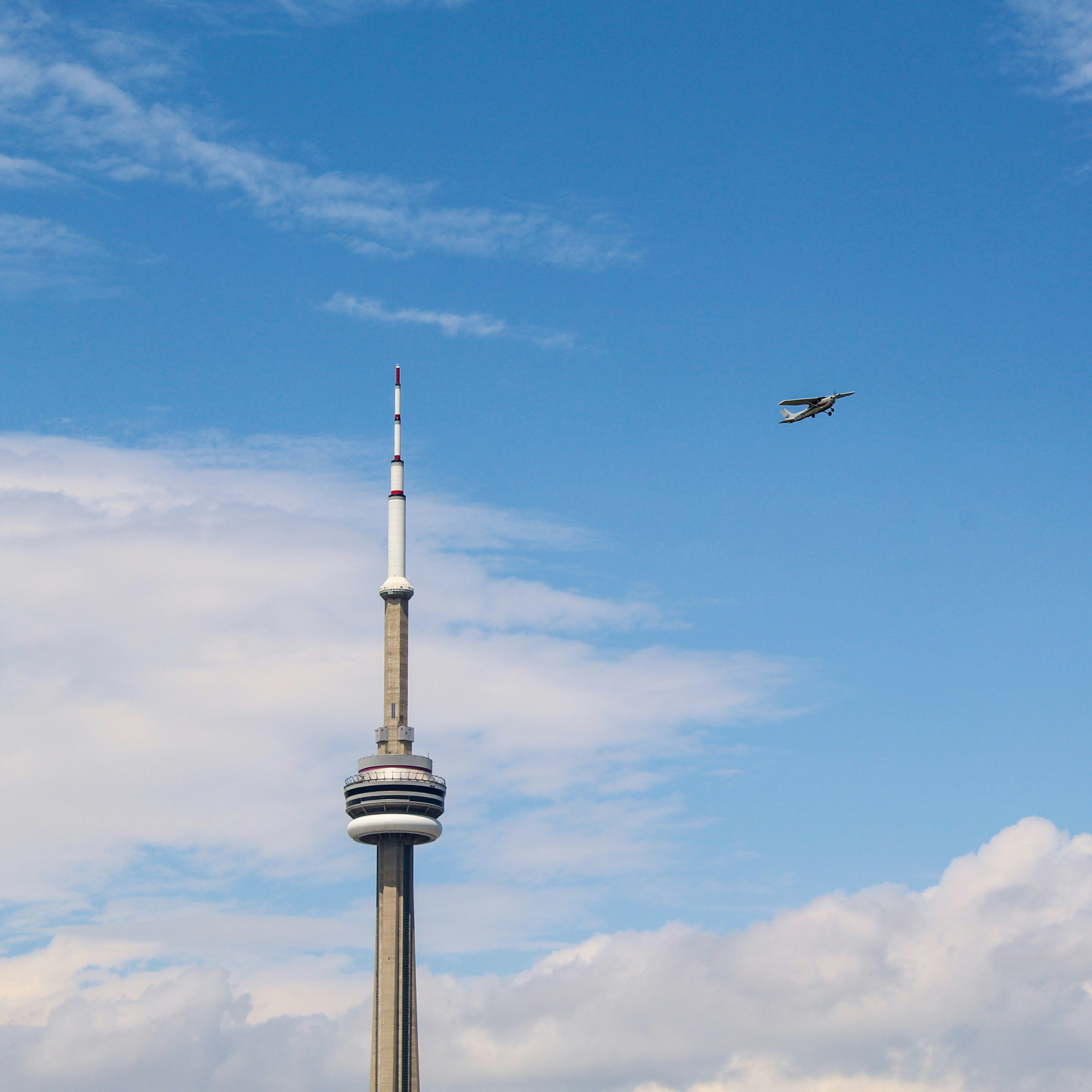 A sleek aircraft glides past the CN Tower under a vibrant blue sky, showcasing the harmony between man-made structures and nature's expanse.