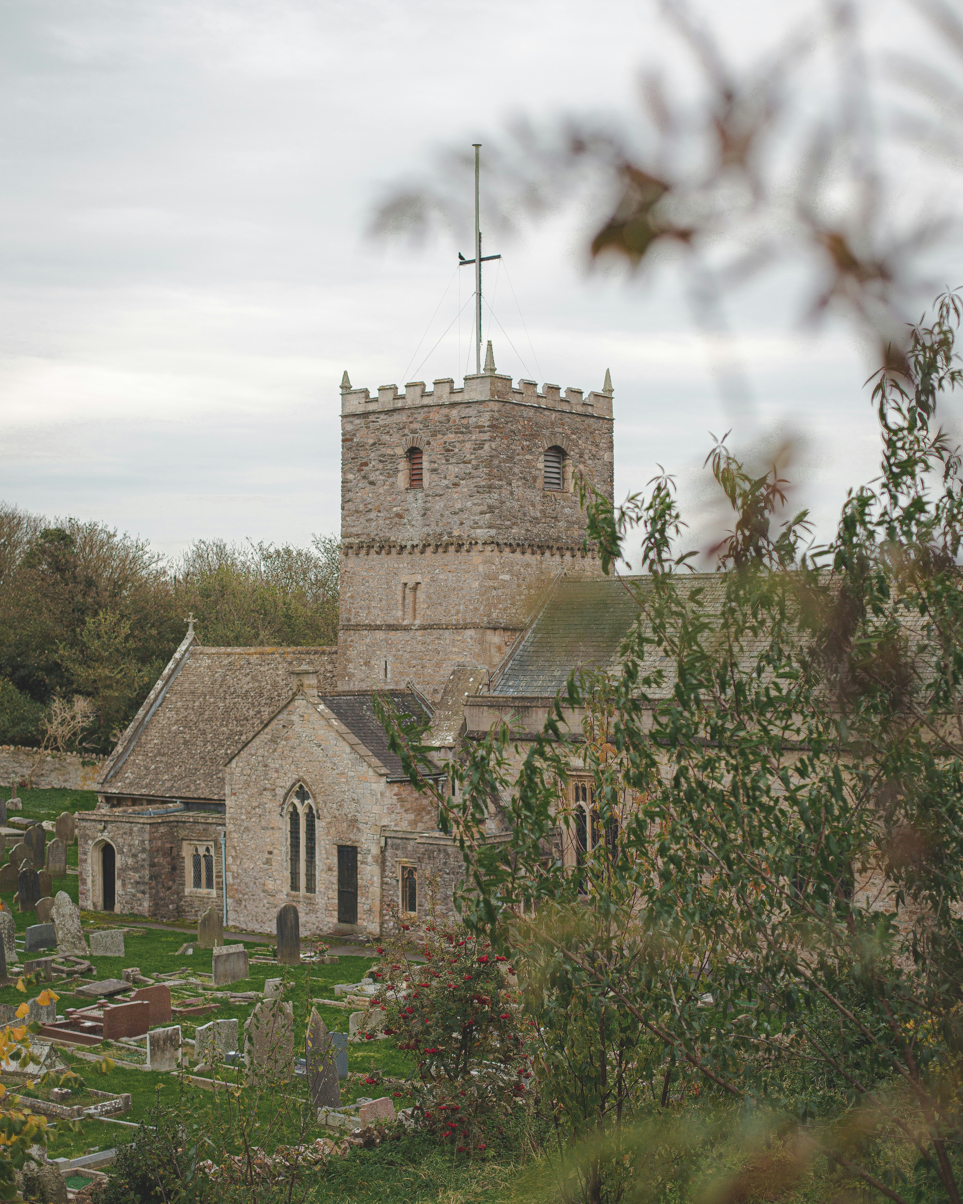 Historic church tower rising above a serene graveyard, surrounded by lush greenery and autumn foliage.