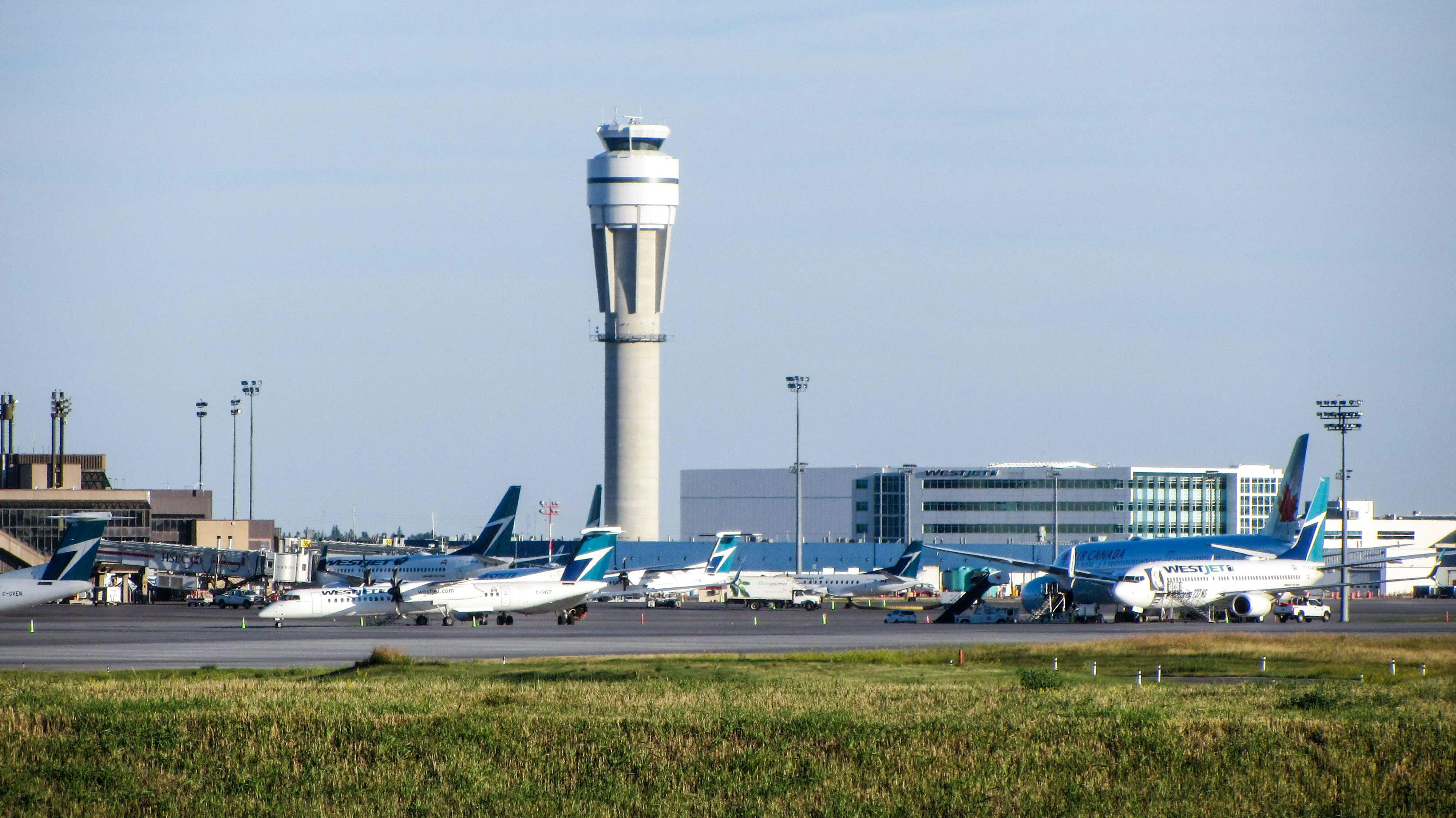 Passenger planes lined up on a runway with a control tower in the background during late afternoon.