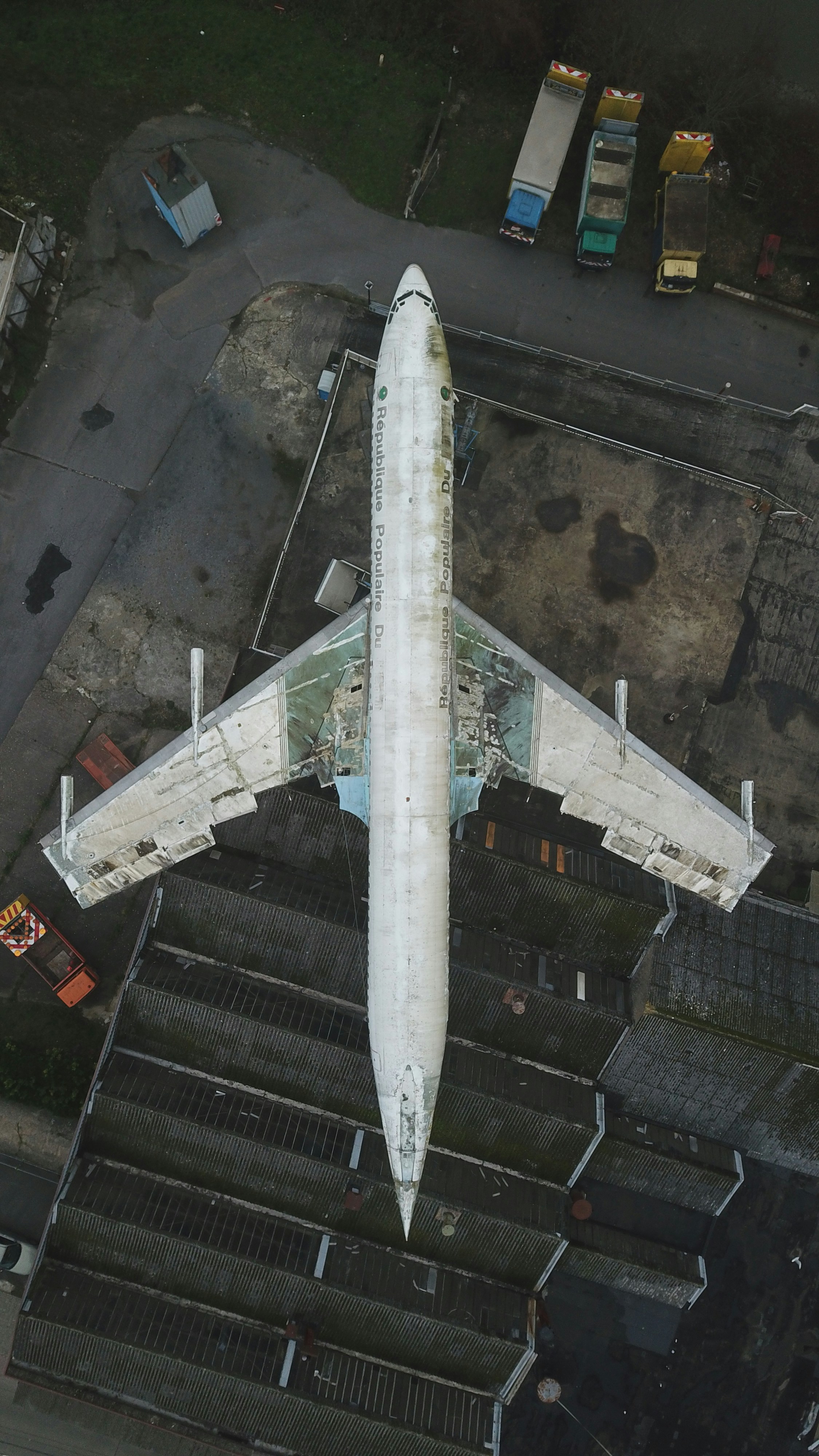 An abandoned aircraft rests on a weathered tarmac, showcasing its worn exterior and intricate details against a backdrop of industrial structures.