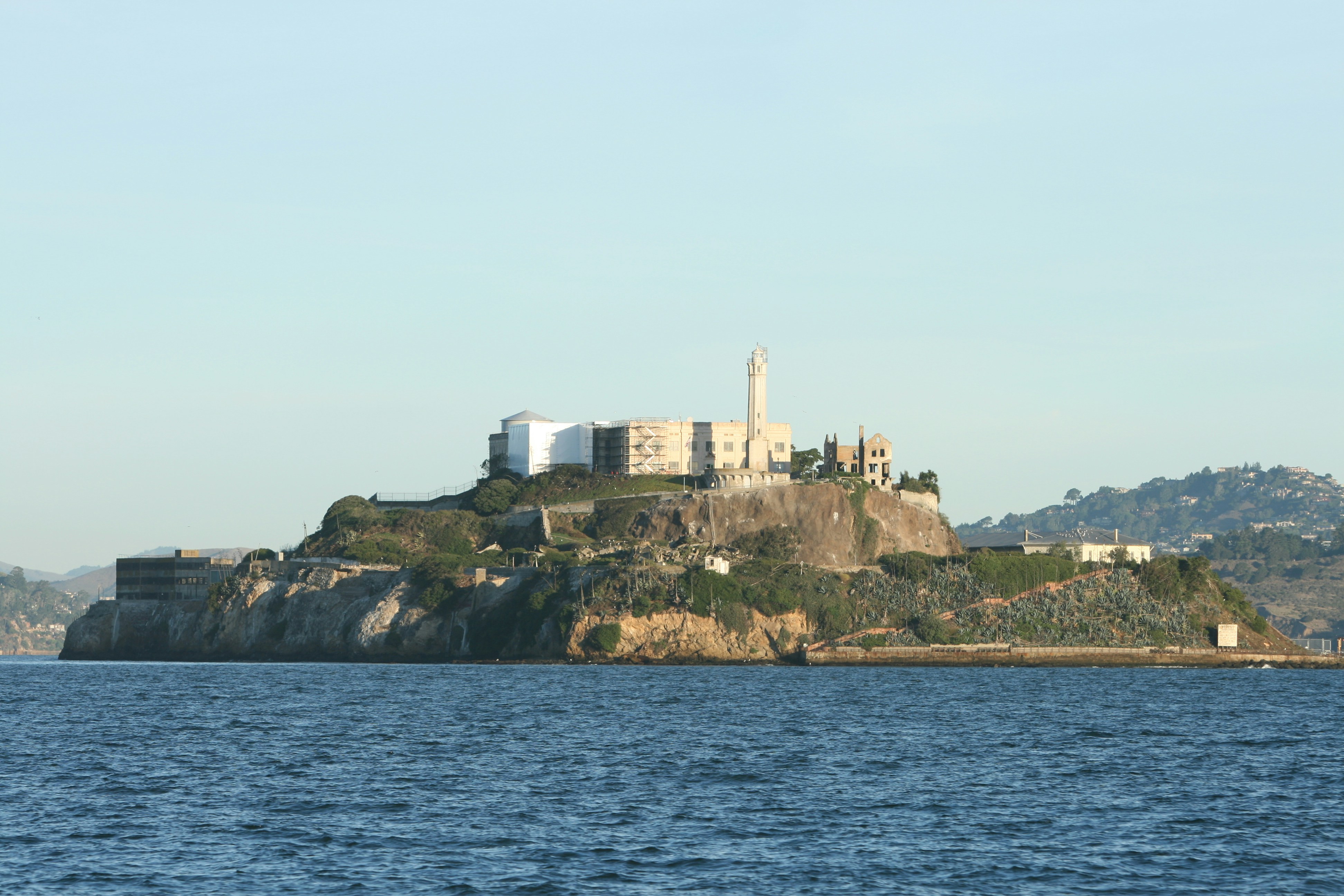 Alcatraz Island stands prominently in the bay, surrounded by water, with its historical buildings visible against the backdrop of a clear sky.