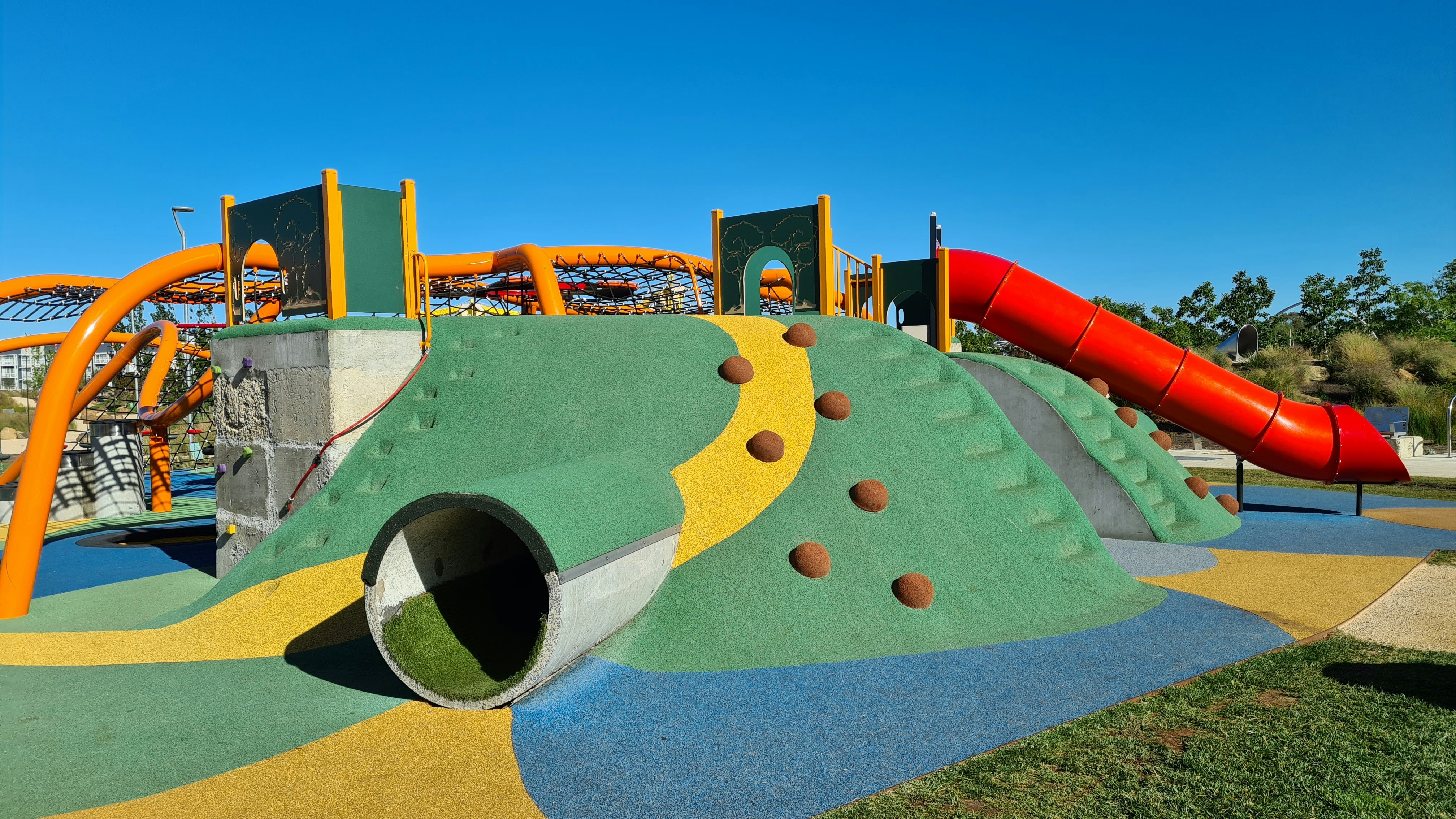 Colorful play structure featuring a slide and climbing hills, designed for children's outdoor fun.