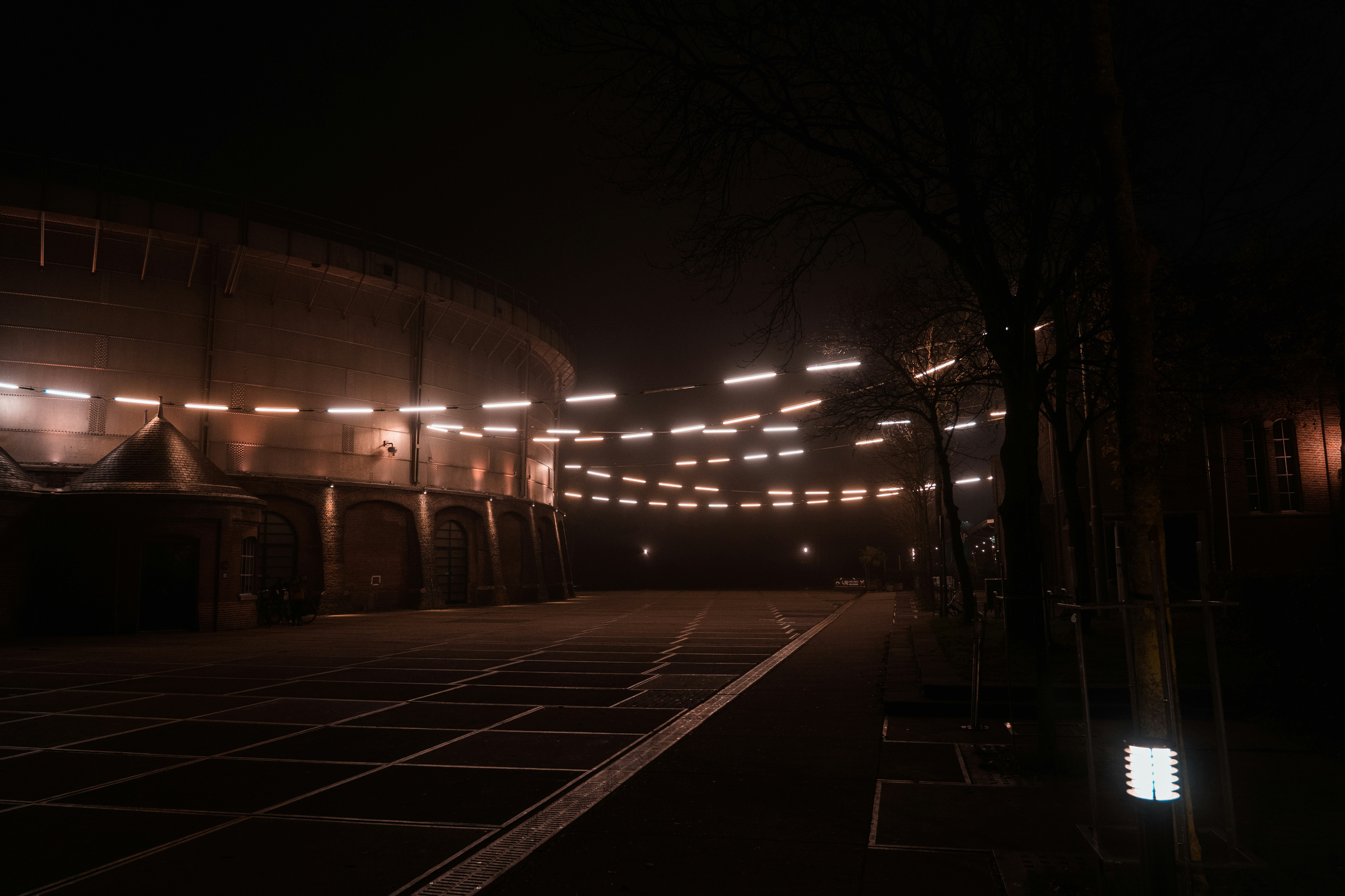 Mysterious urban landscape featuring softly glowing lights strung across a deserted space, creating an atmospheric ambiance. The scene captures the essence of solitude in a modern setting.