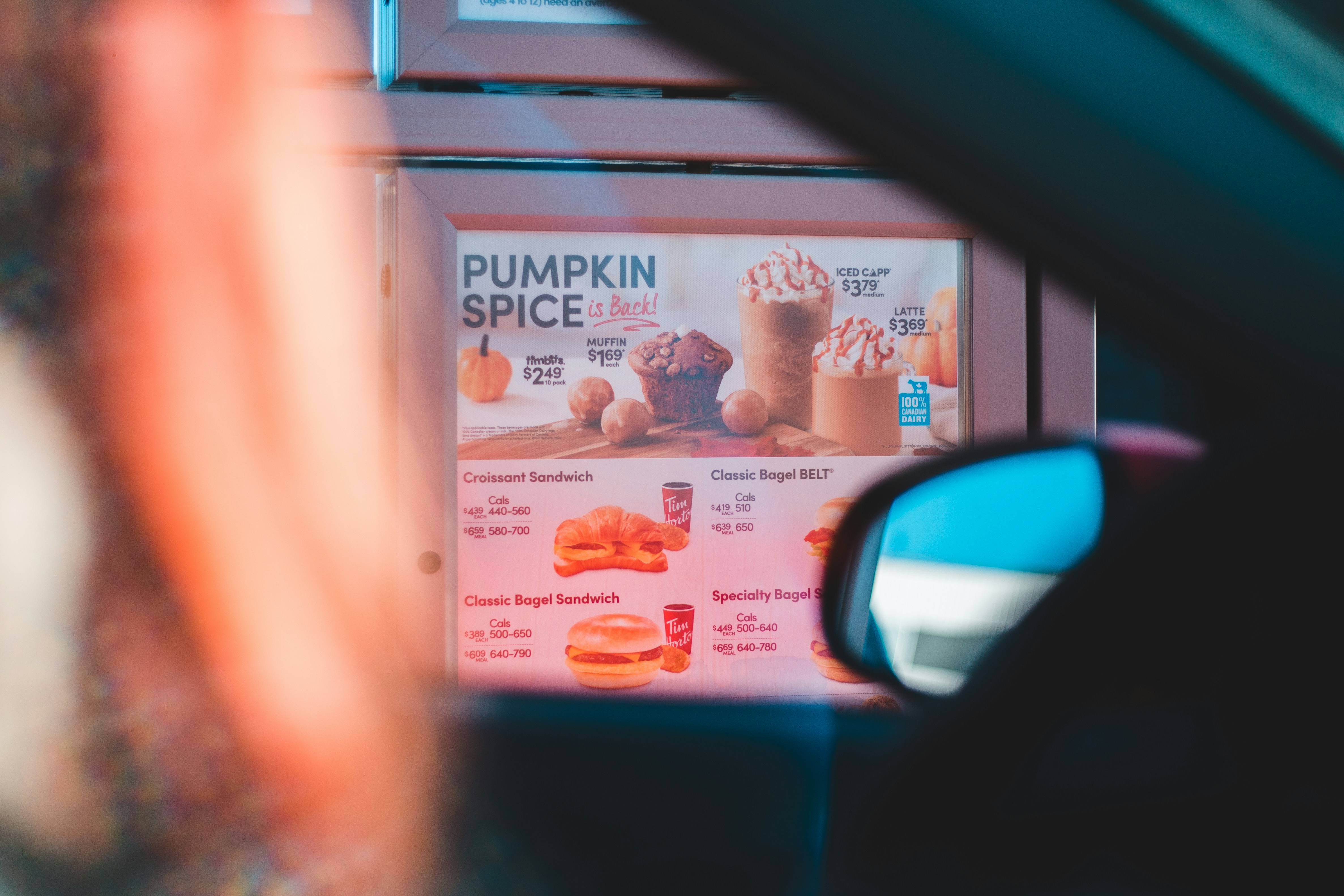 Promotional menu featuring seasonal pumpkin spice items at a drive-thru, with a blurred view of a car interior in the foreground.