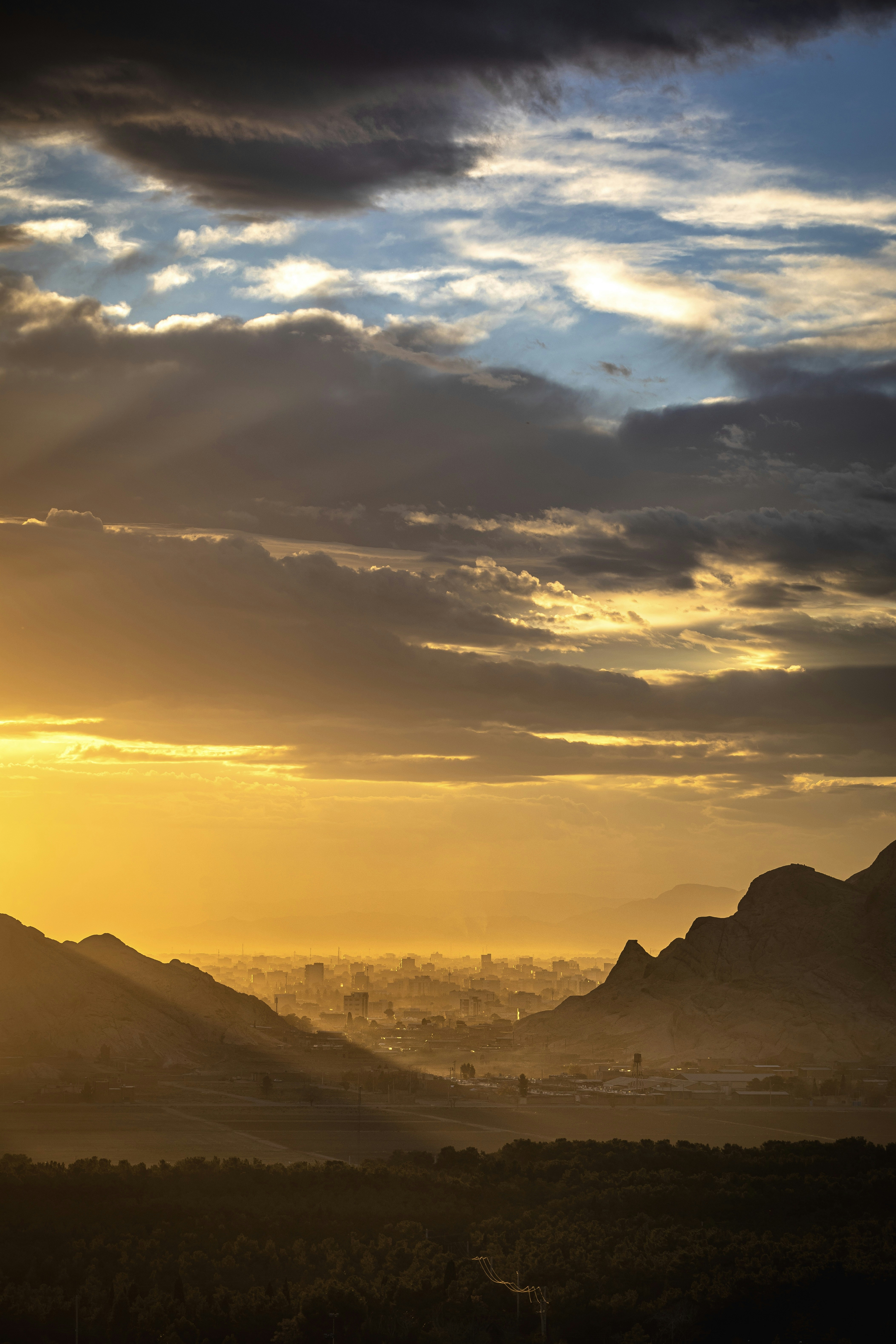 Vibrant sunset illuminating a city skyline nestled between mountains, with dramatic clouds enhancing the scene's depth.