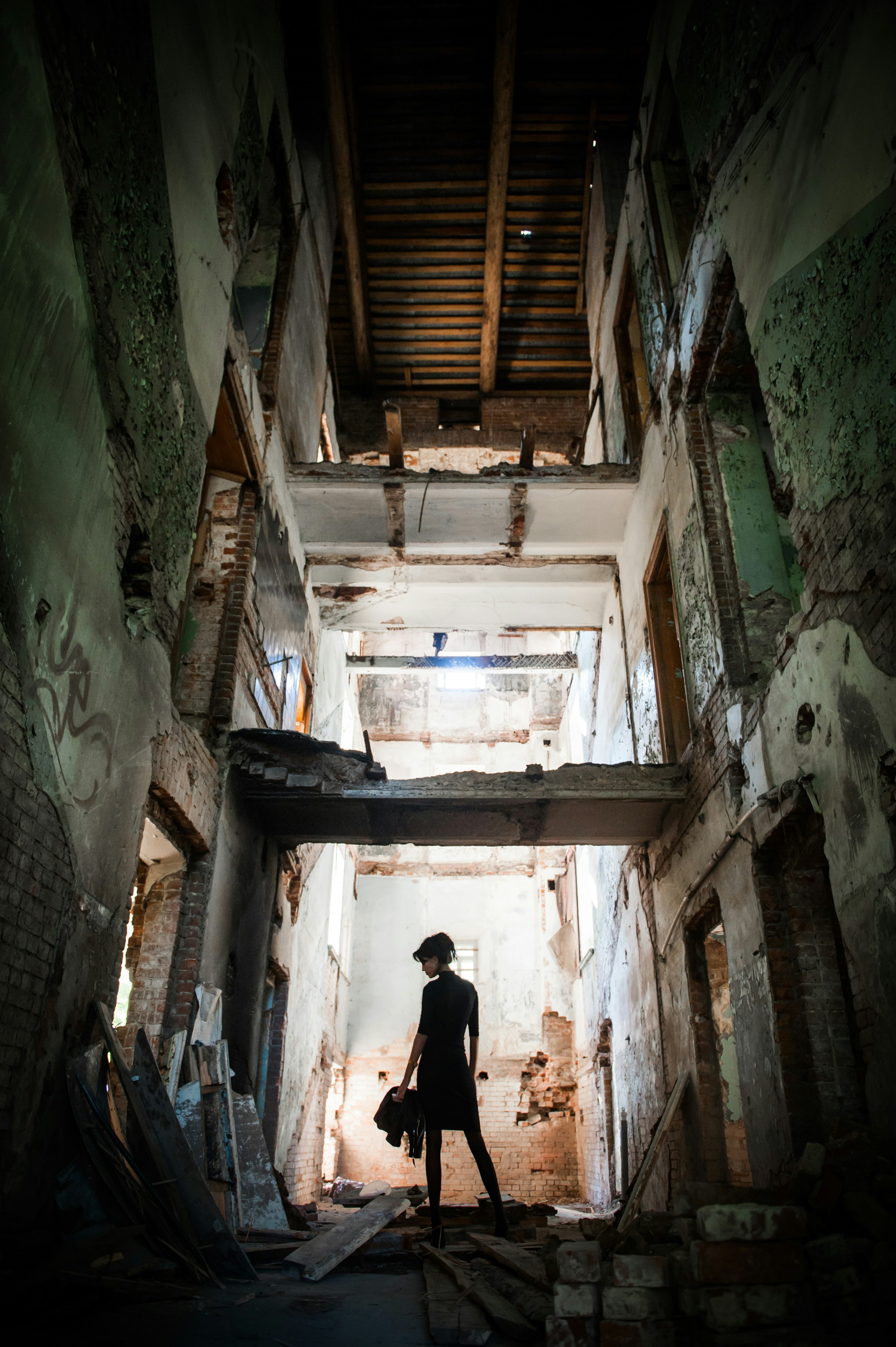 Silhouette of a figure standing in a decaying interior of an abandoned building, with light streaming through broken windows.