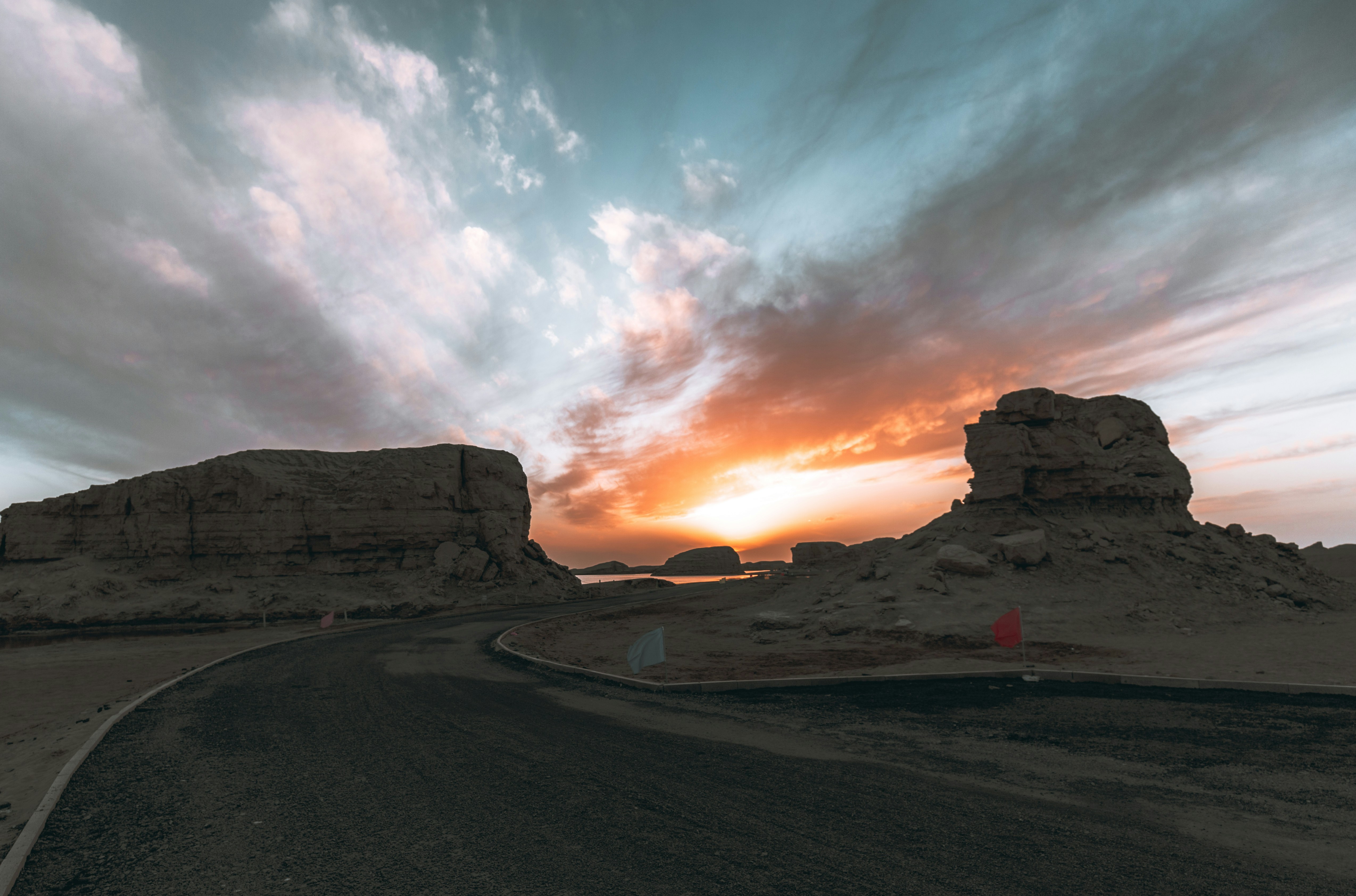Sunset illuminates towering rock formations flanking a winding desert road under a dramatic sky.