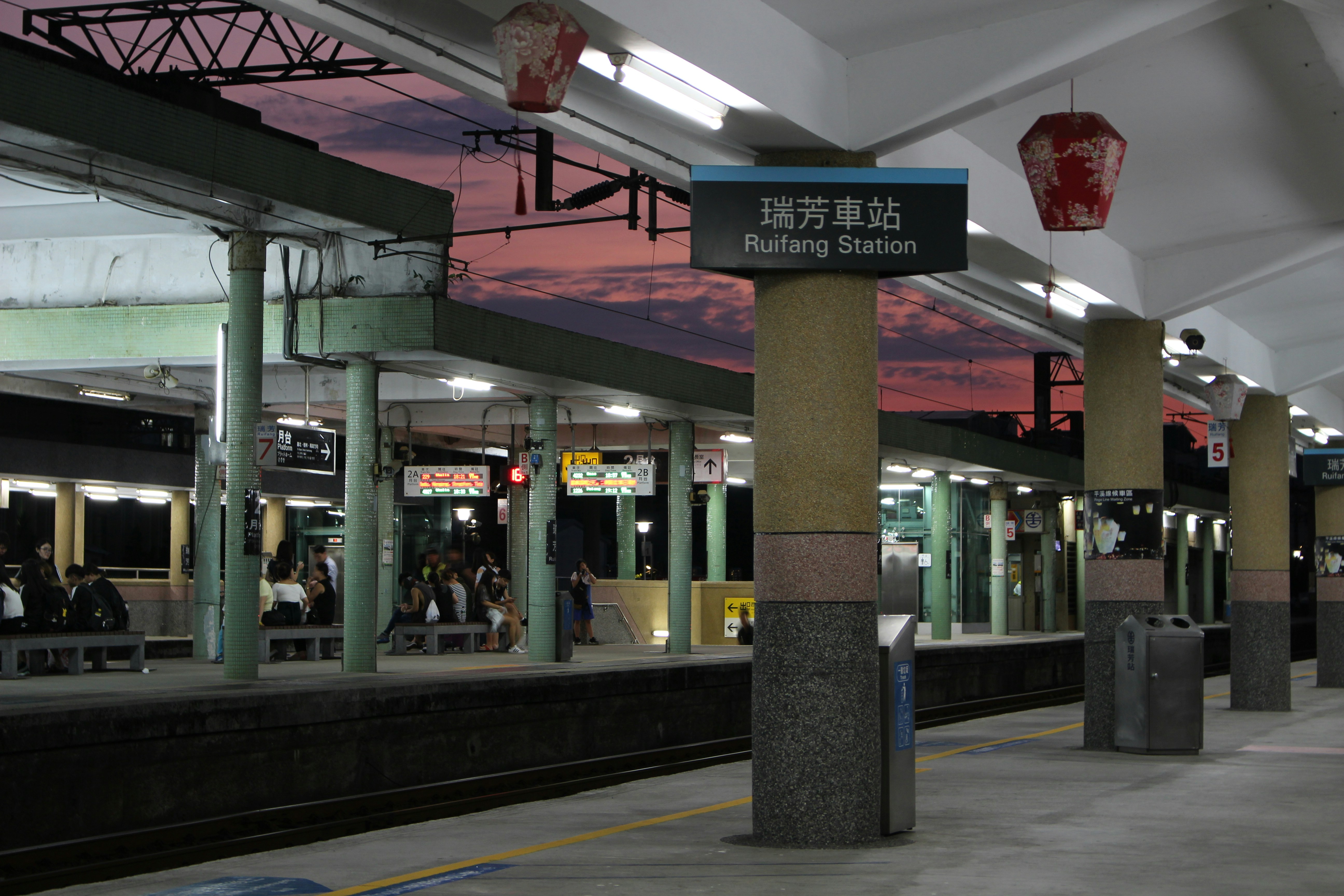Ruifang Station platform illuminated under a twilight sky, with passengers waiting and vibrant colors reflecting the day's end.