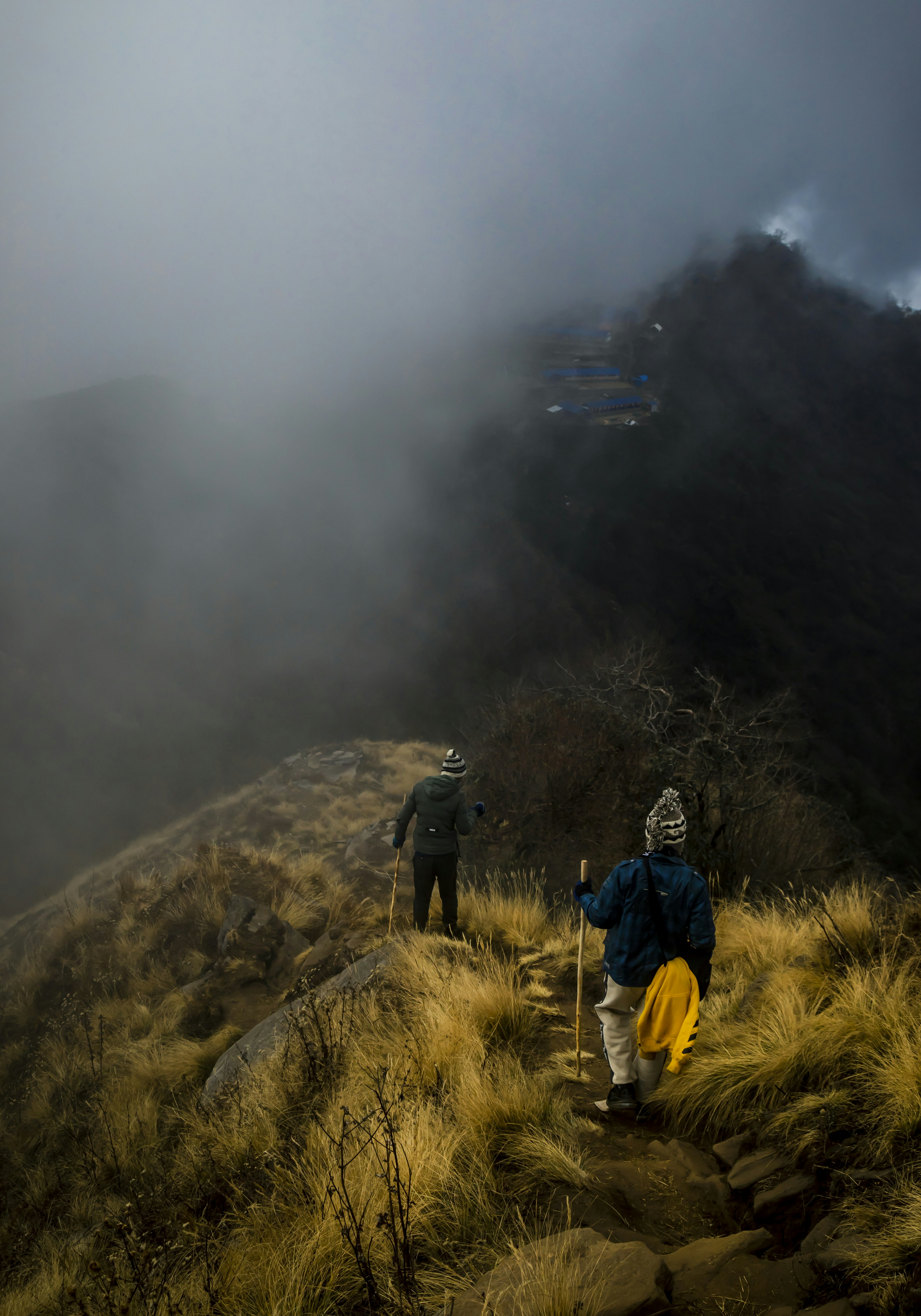 Two hikers tread a misty ridge as dusk drapes the valley
